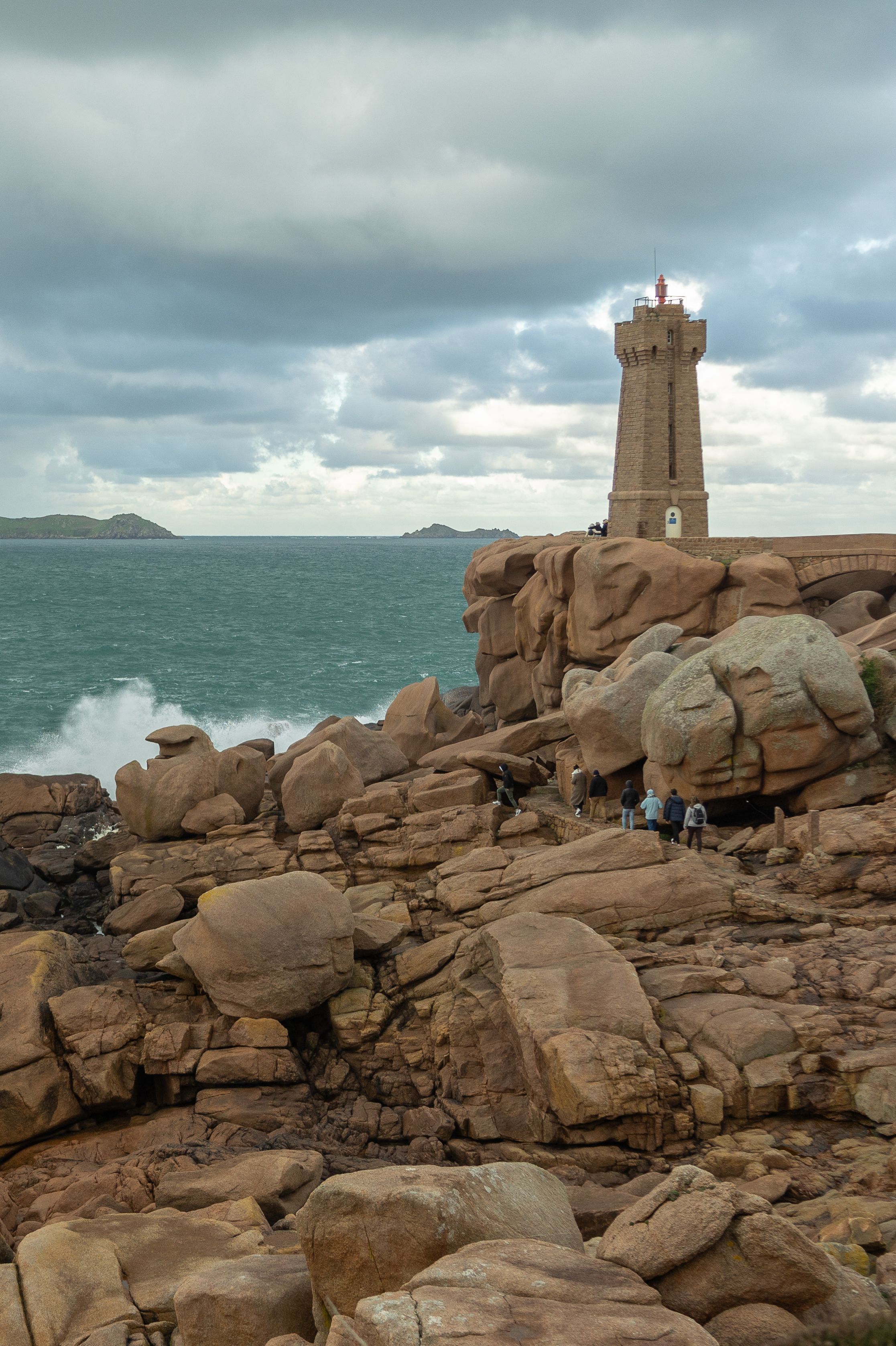 A lighthouse on a rocky shore with a cloudy sky · Free Stock Photo