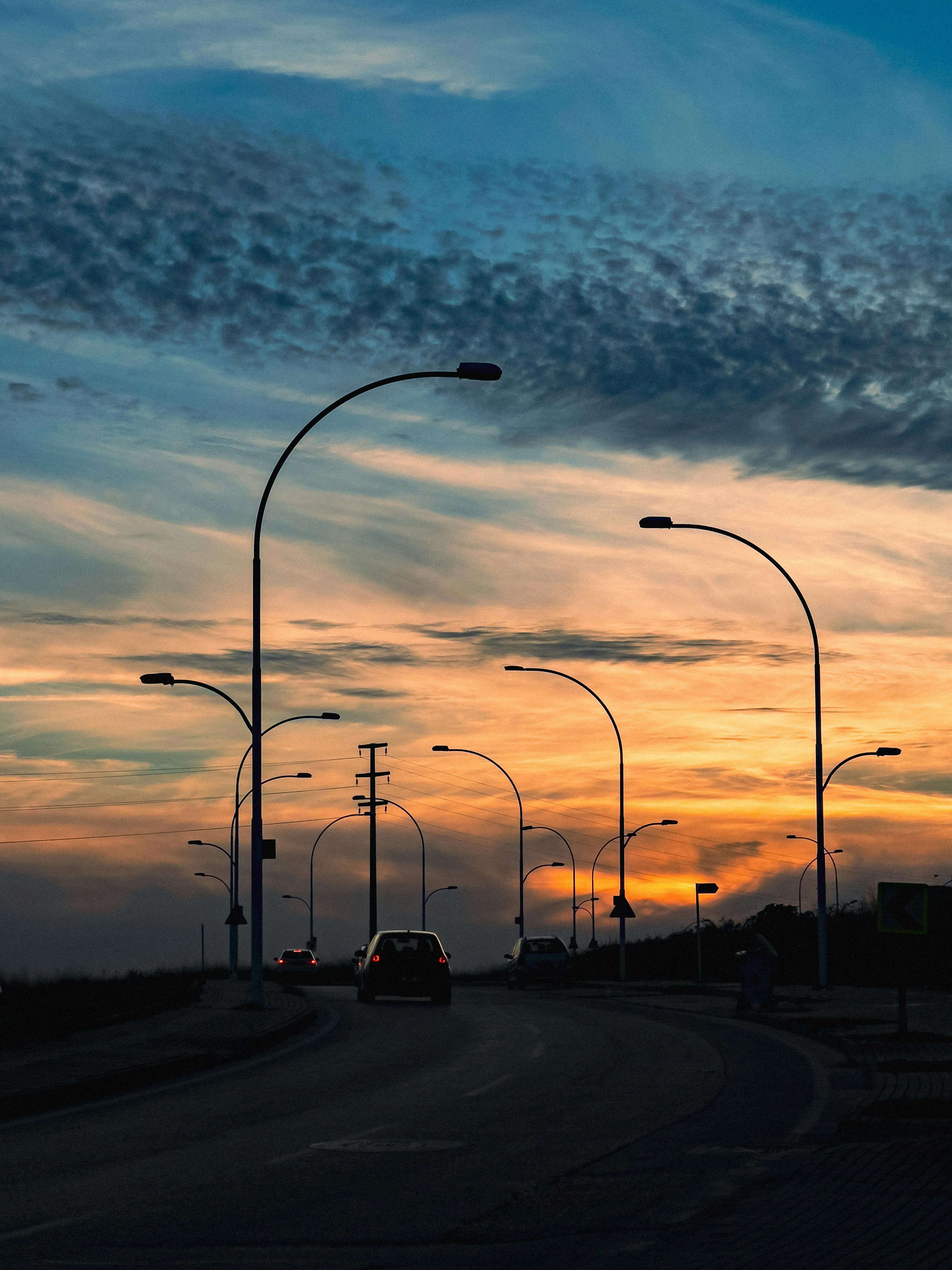 A sunset over a road with street lights · Free Stock Photo