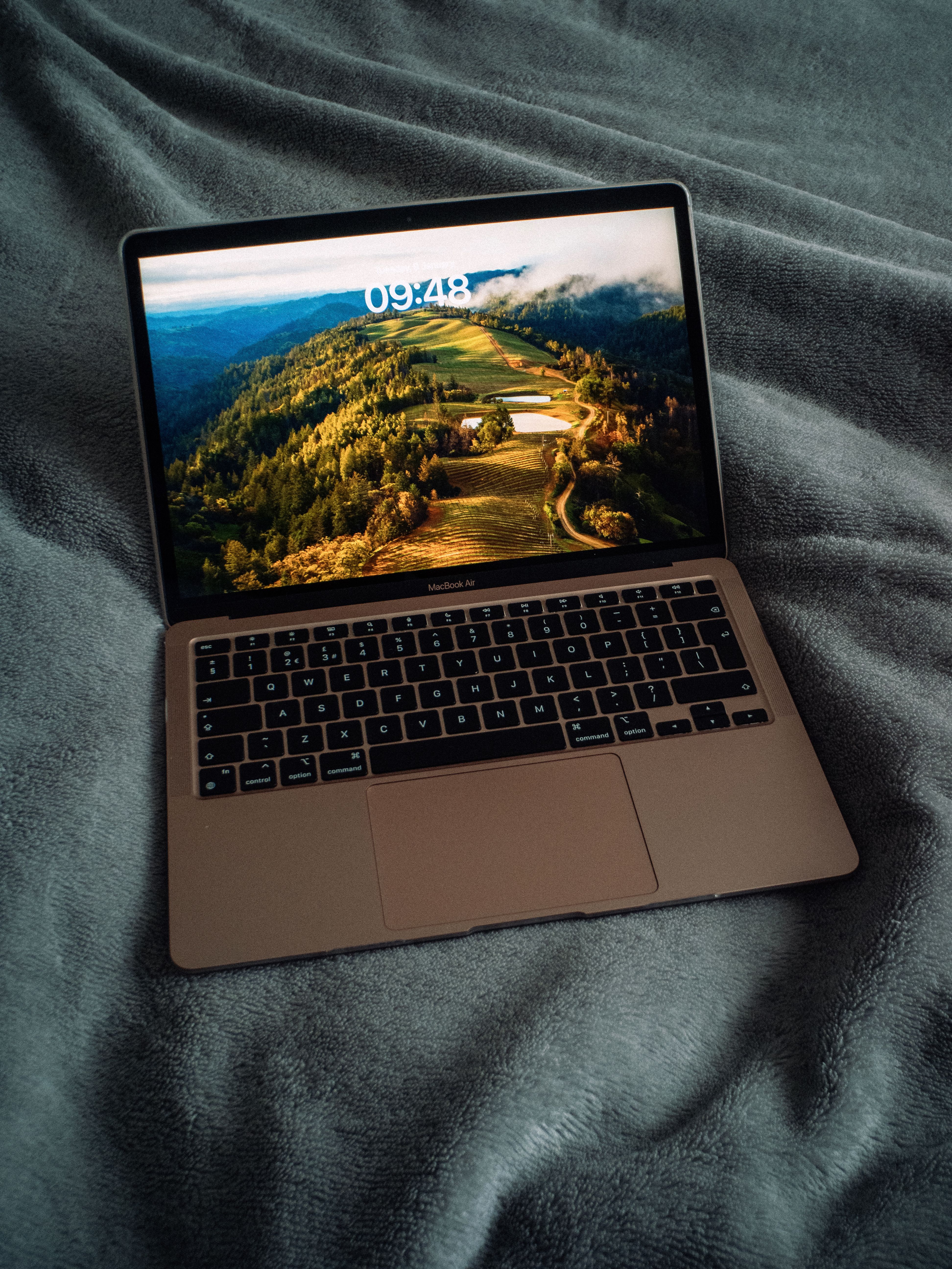 A laptop computer on a bed with a landscape photo · Free Stock Photo