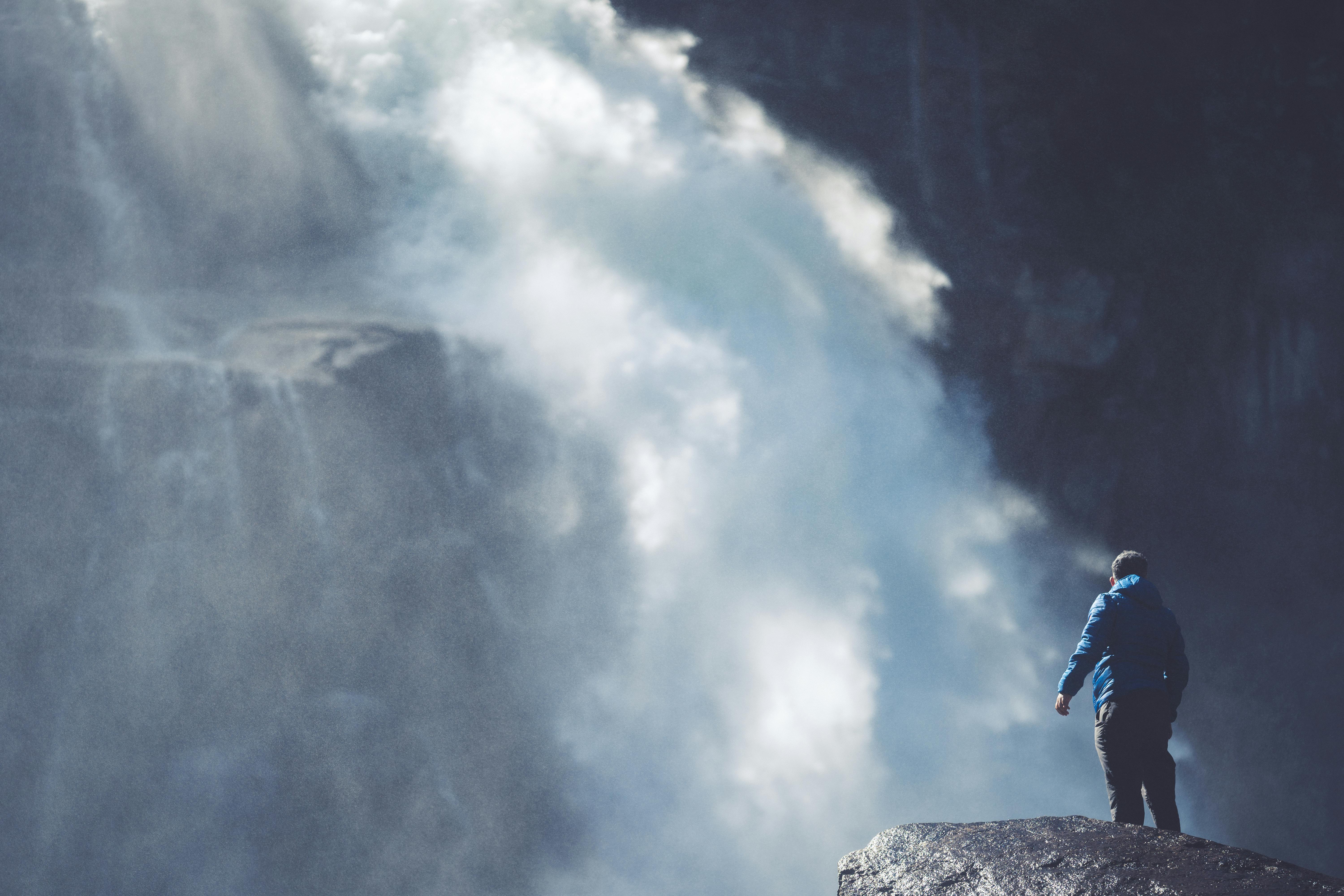 Hiker Standing on a Rock Overhang Admiring a Waterfall · Free Stock Photo