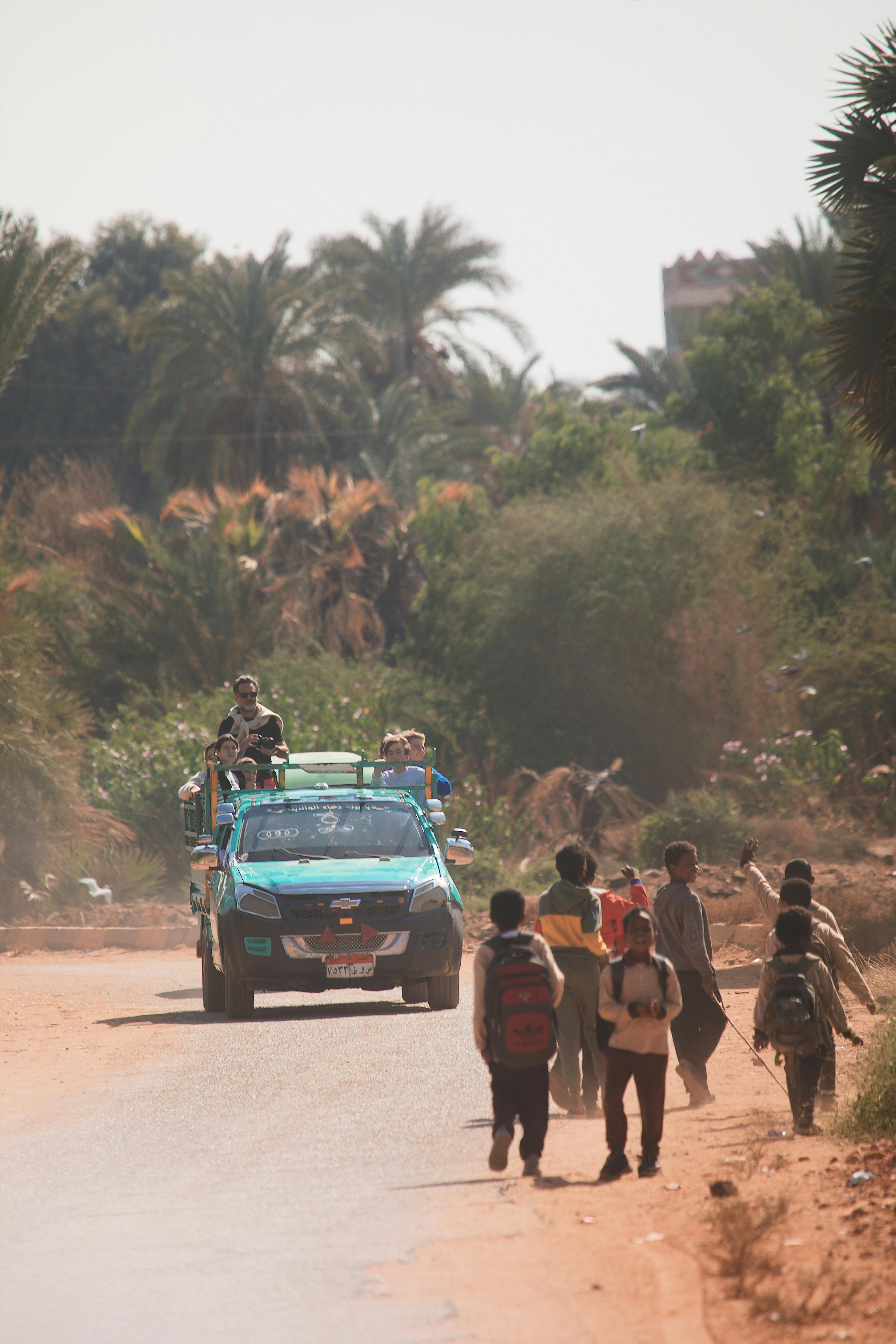A group of people walking down a road with a car · Free Stock Photo