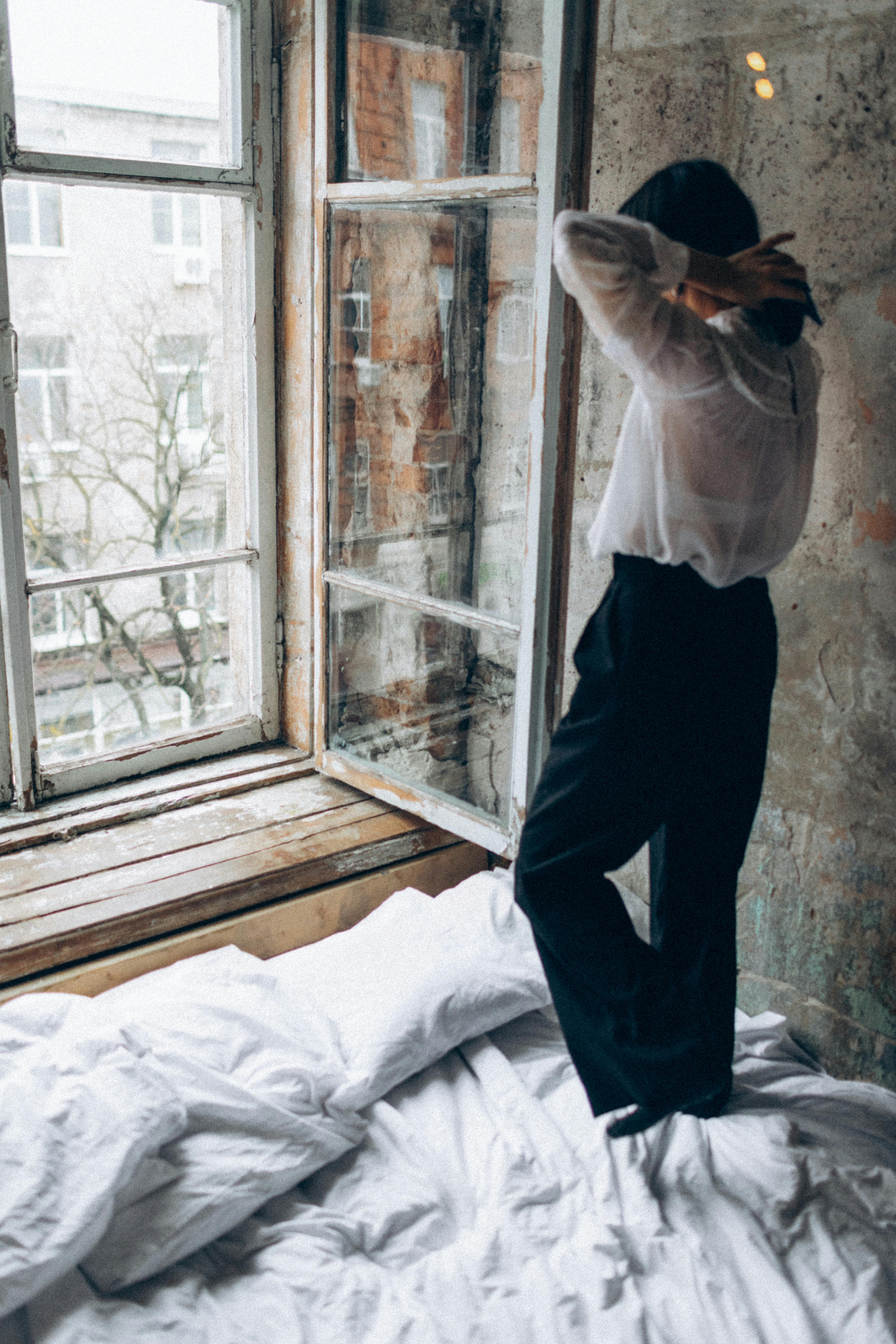 Woman Standing on Bed and Looking into Window · Free Stock Photo