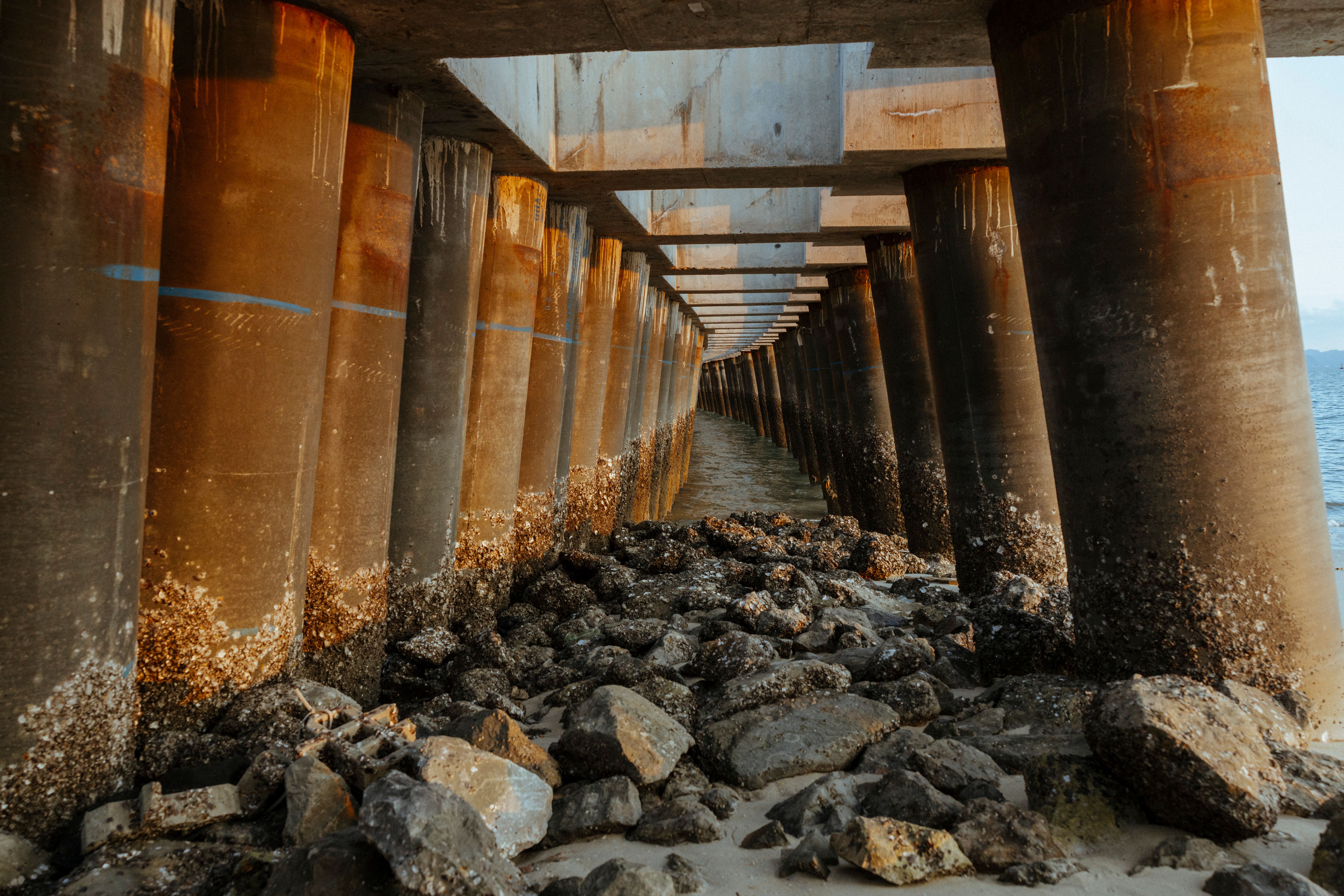 The underside of a pier with rocks and sand · Free Stock Photo