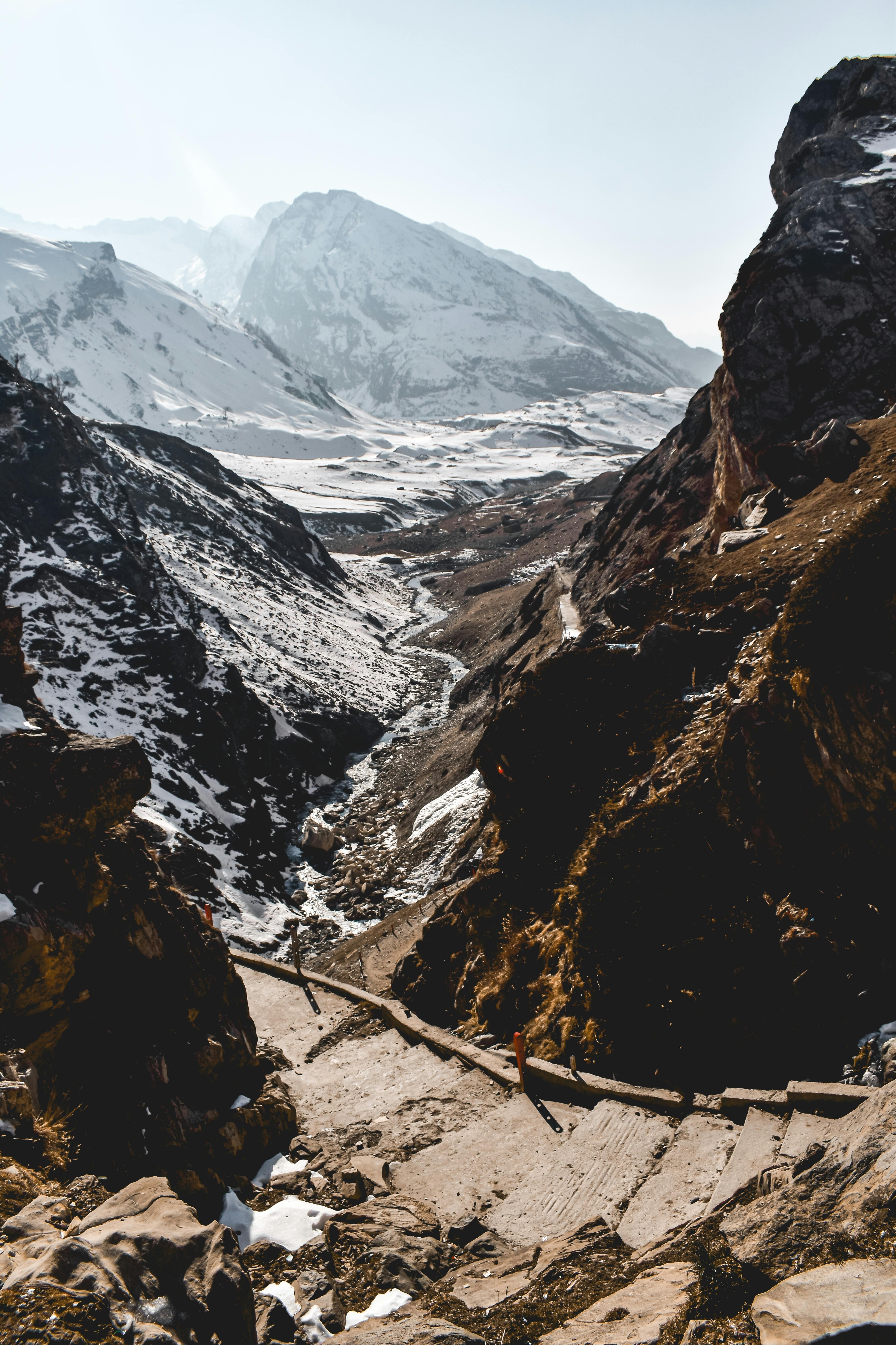 A person walking down a mountain path with snow covered mountains in ...