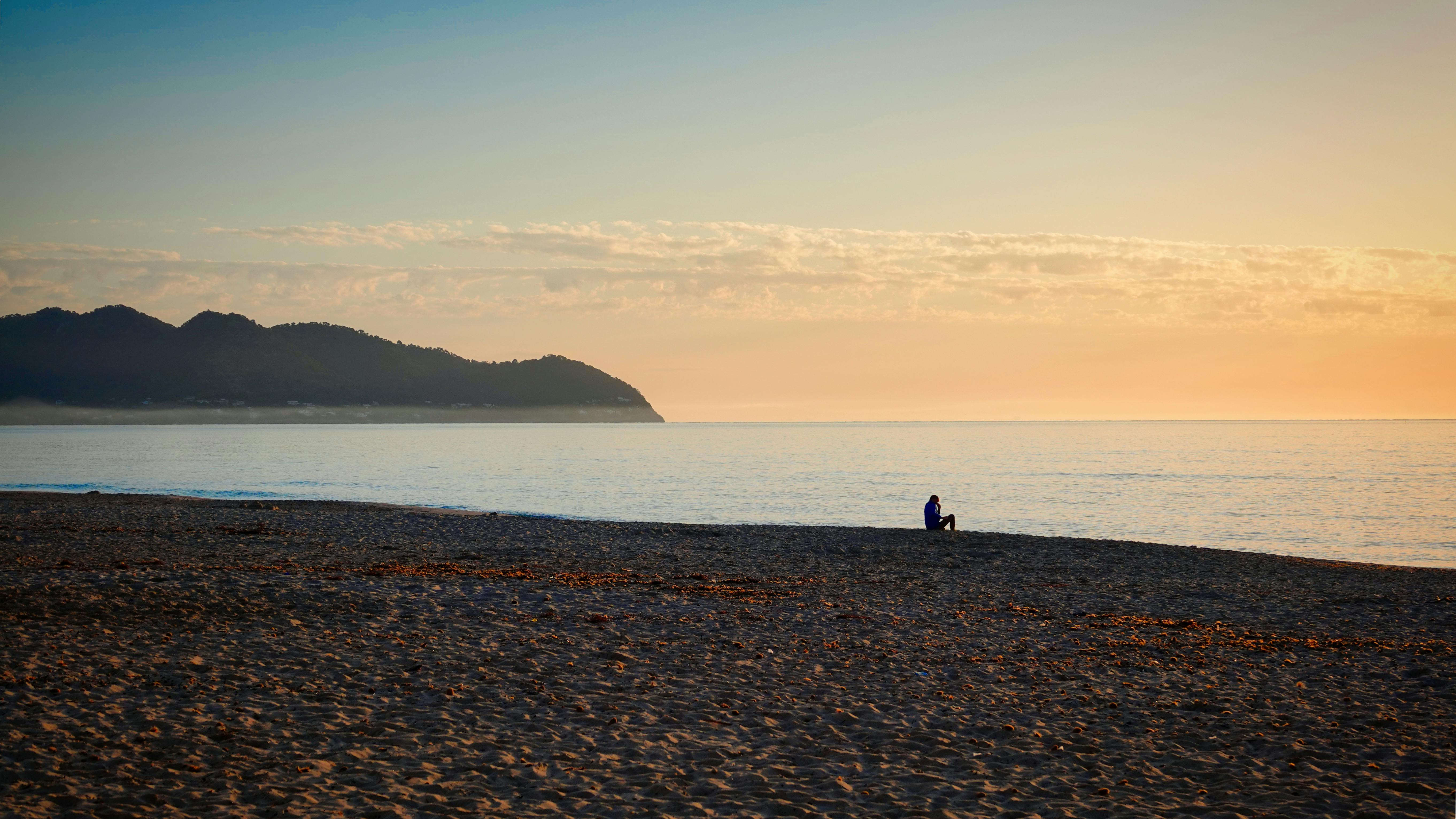Person Sitting on Beach at Sunset · Free Stock Photo