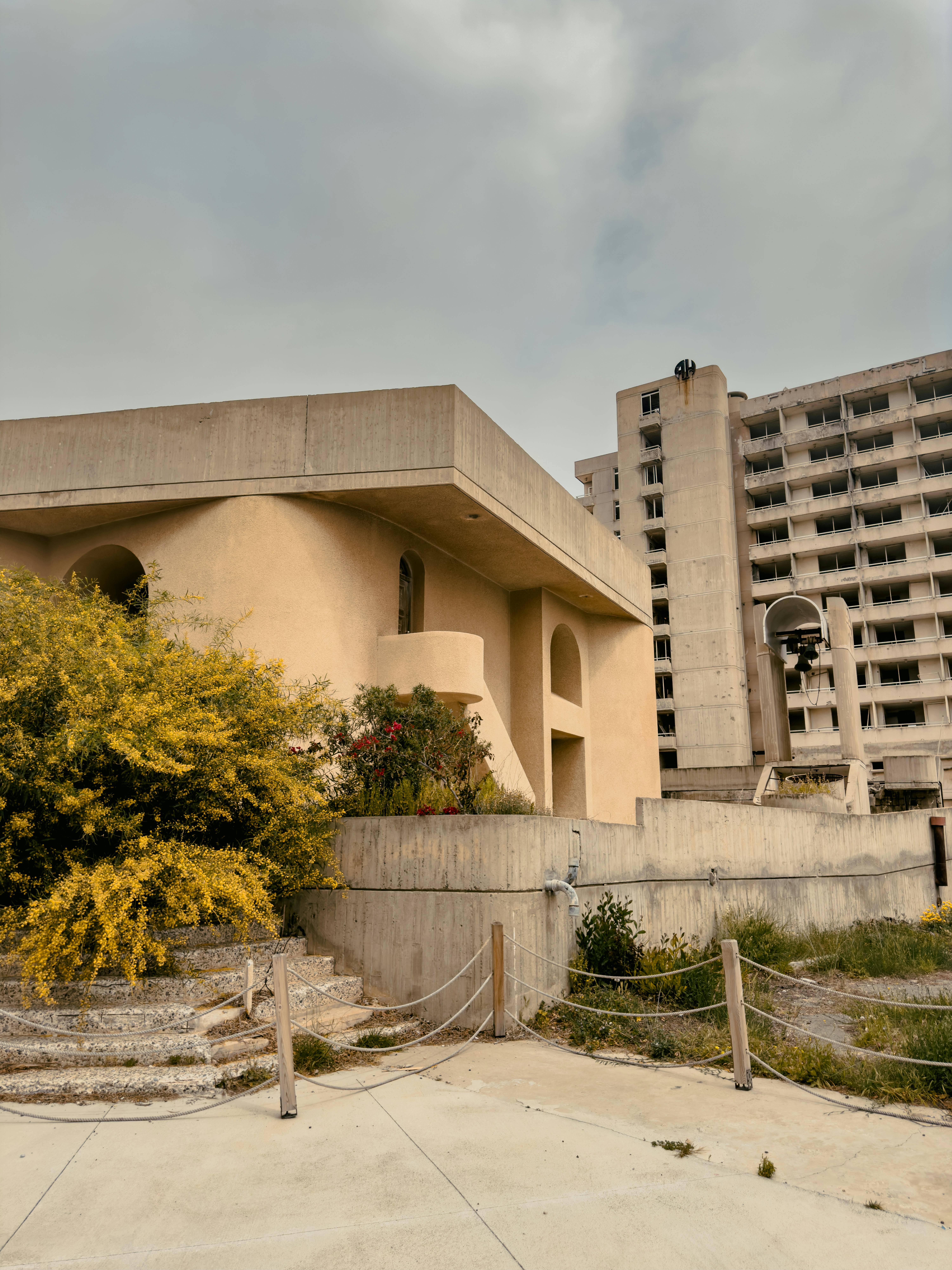 A building with a large concrete structure and a tree · Free Stock Photo
