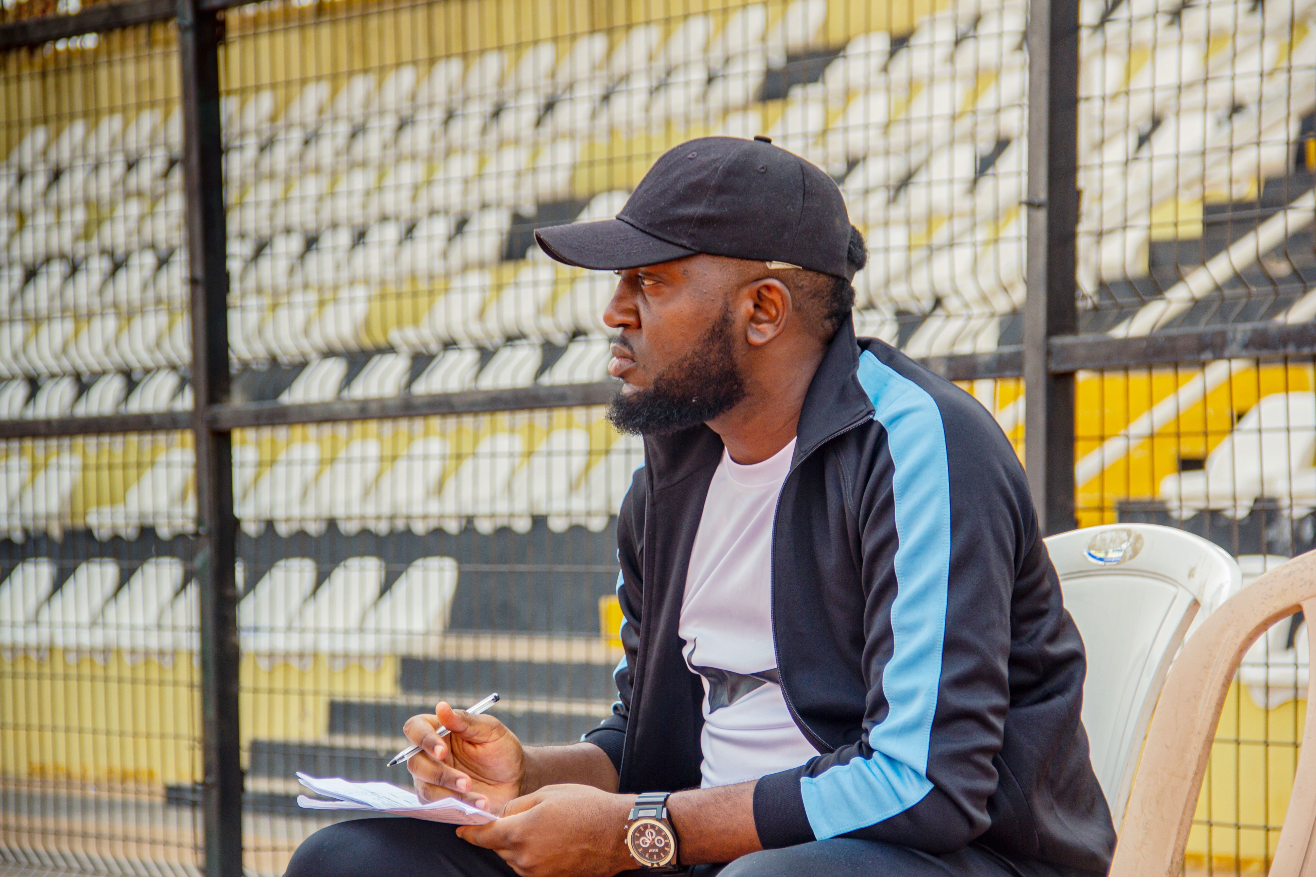 Man in Cap Sitting and Taking Notes at Stadium · Free Stock Photo