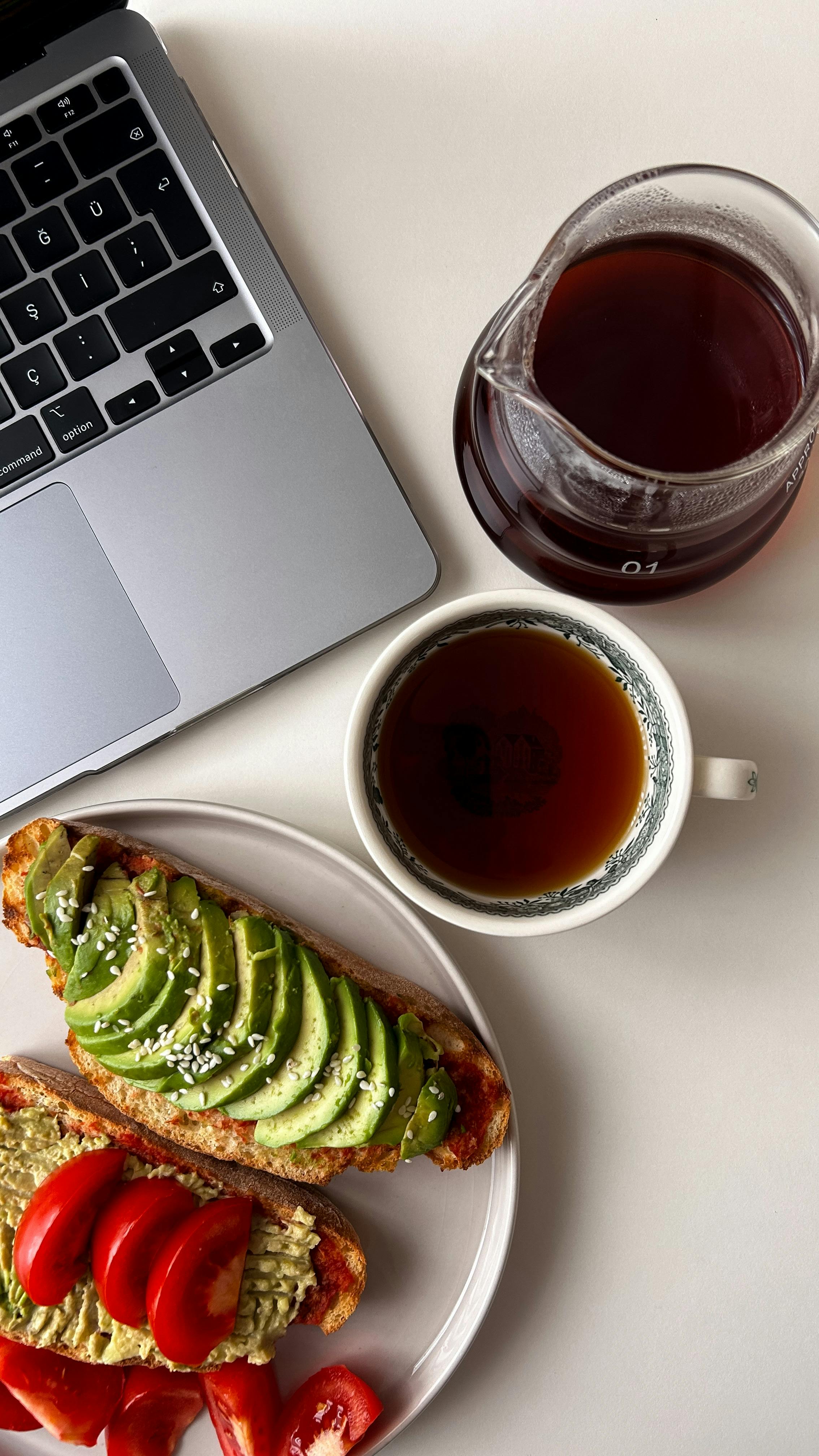 A laptop, coffee and toast with avocado and tomato · Free Stock Photo