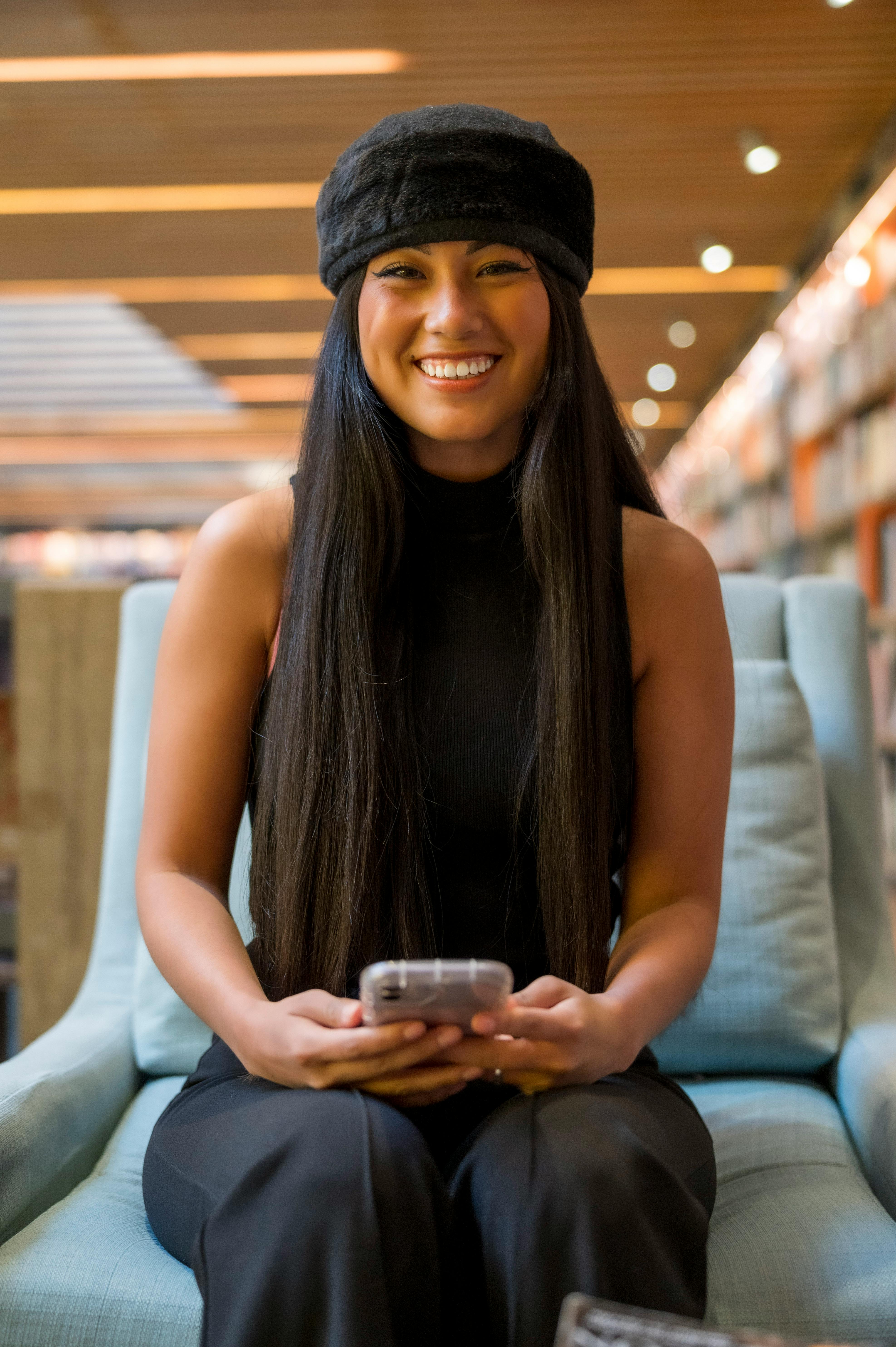 A woman in a black beanie sitting in a chair holding a cell phone ...