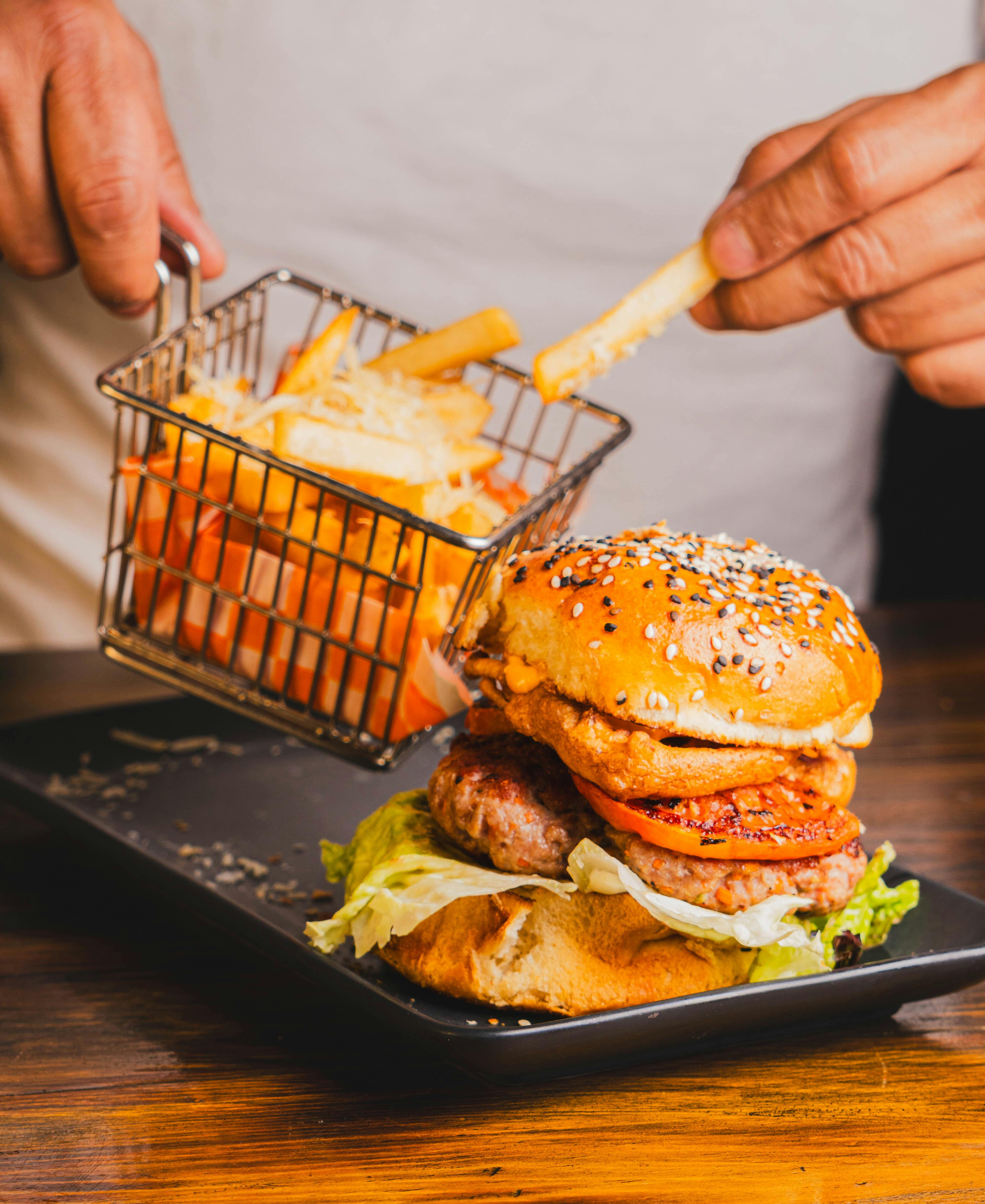 Man Hands Holding Fries over Burger · Free Stock Photo