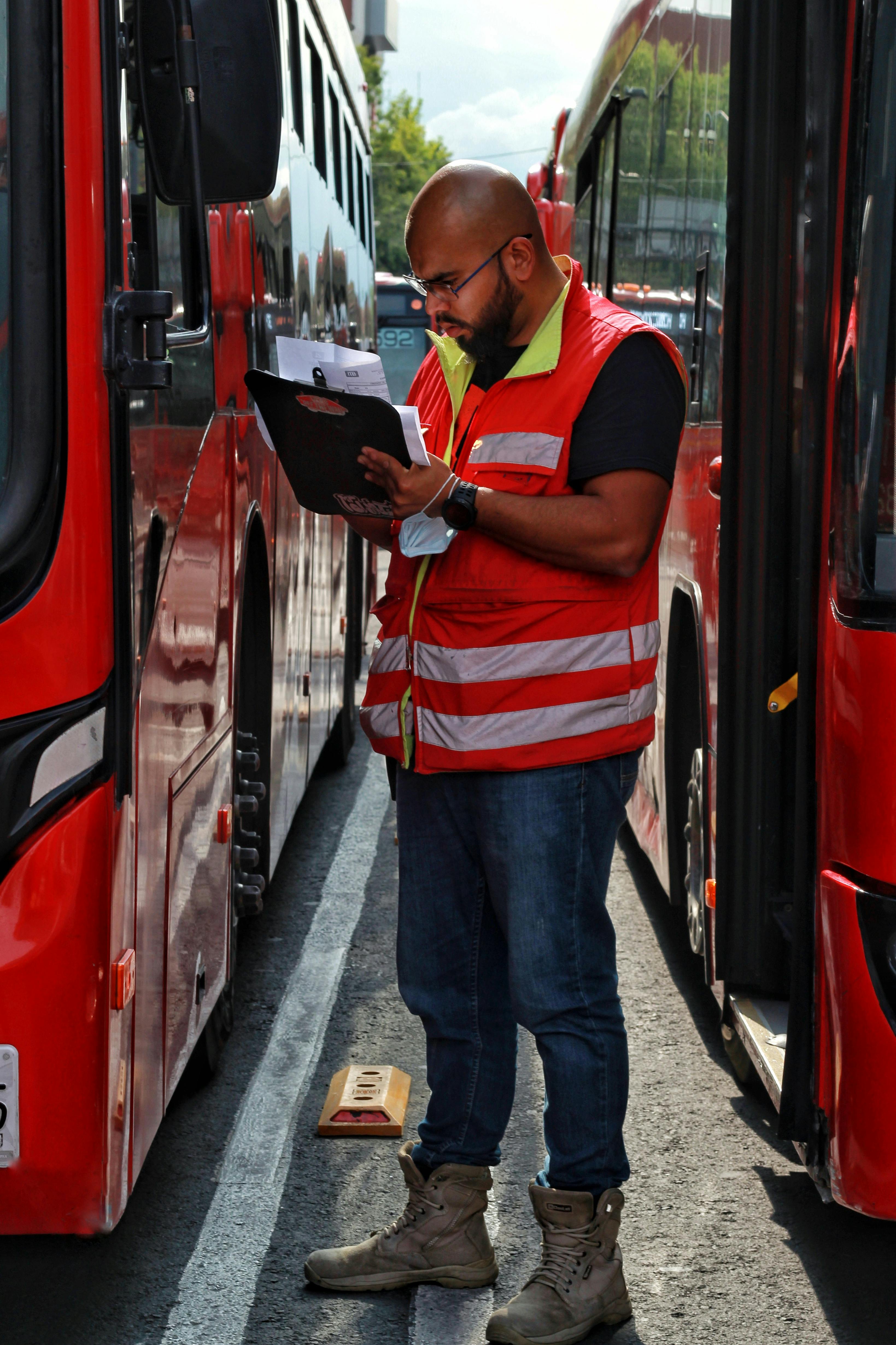 A man in a safety vest is looking at a bus · Free Stock Photo