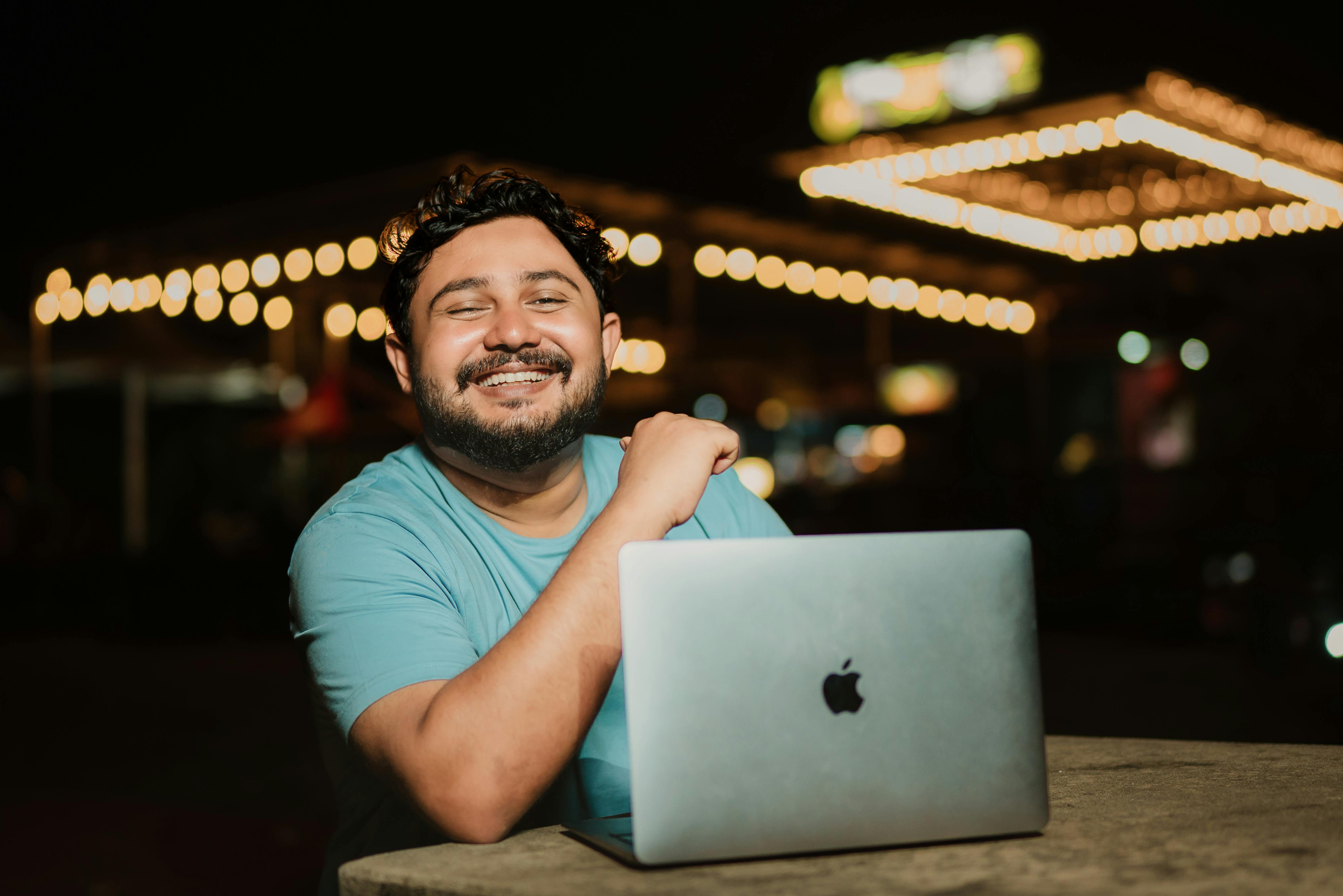 Cheerful Geek Sitting with Laptop at Table · Free Stock Photo