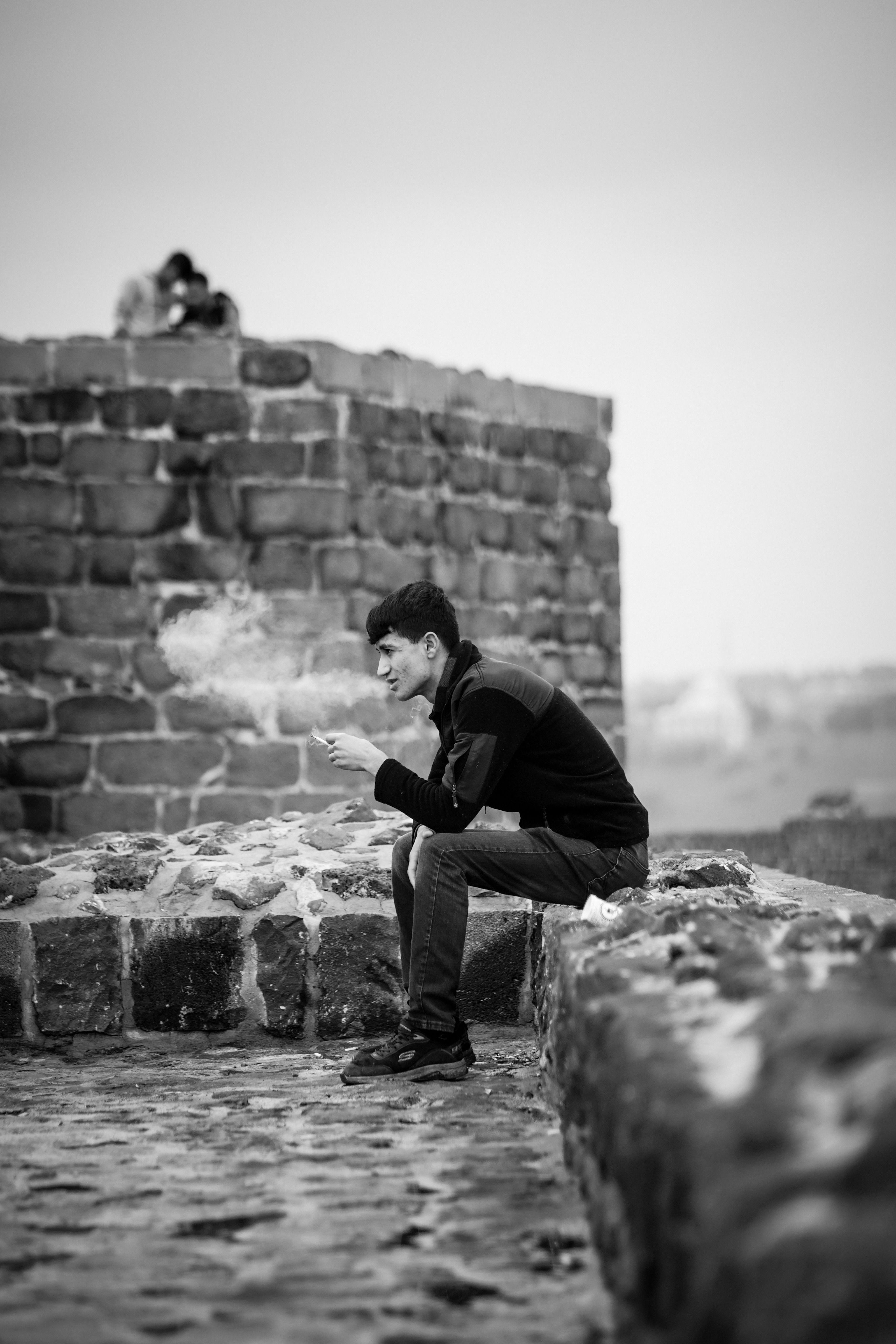 A man sitting on a wall smoking a cigarette · Free Stock Photo