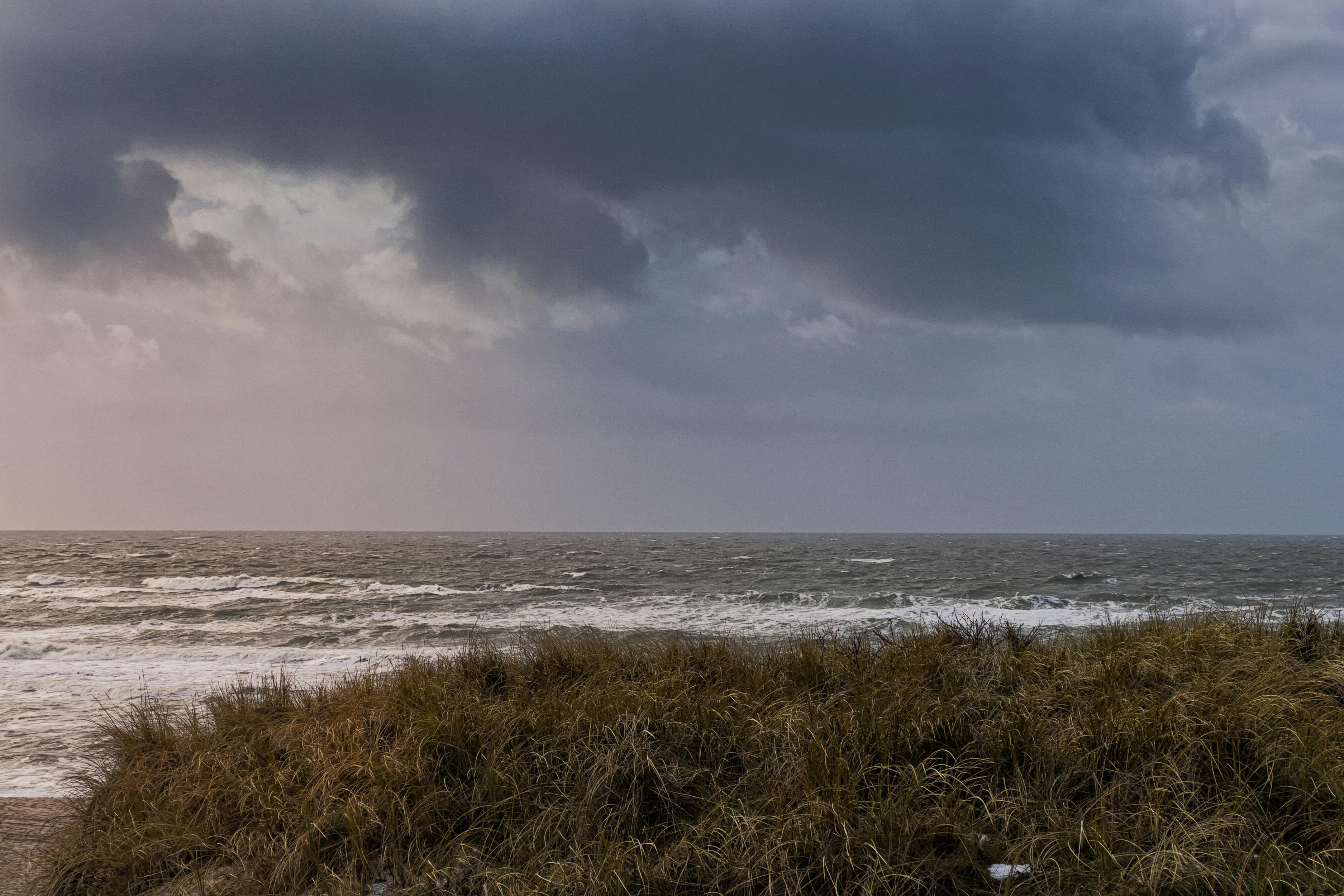 A lone person standing on the beach with a stormy sky · Free Stock Photo
