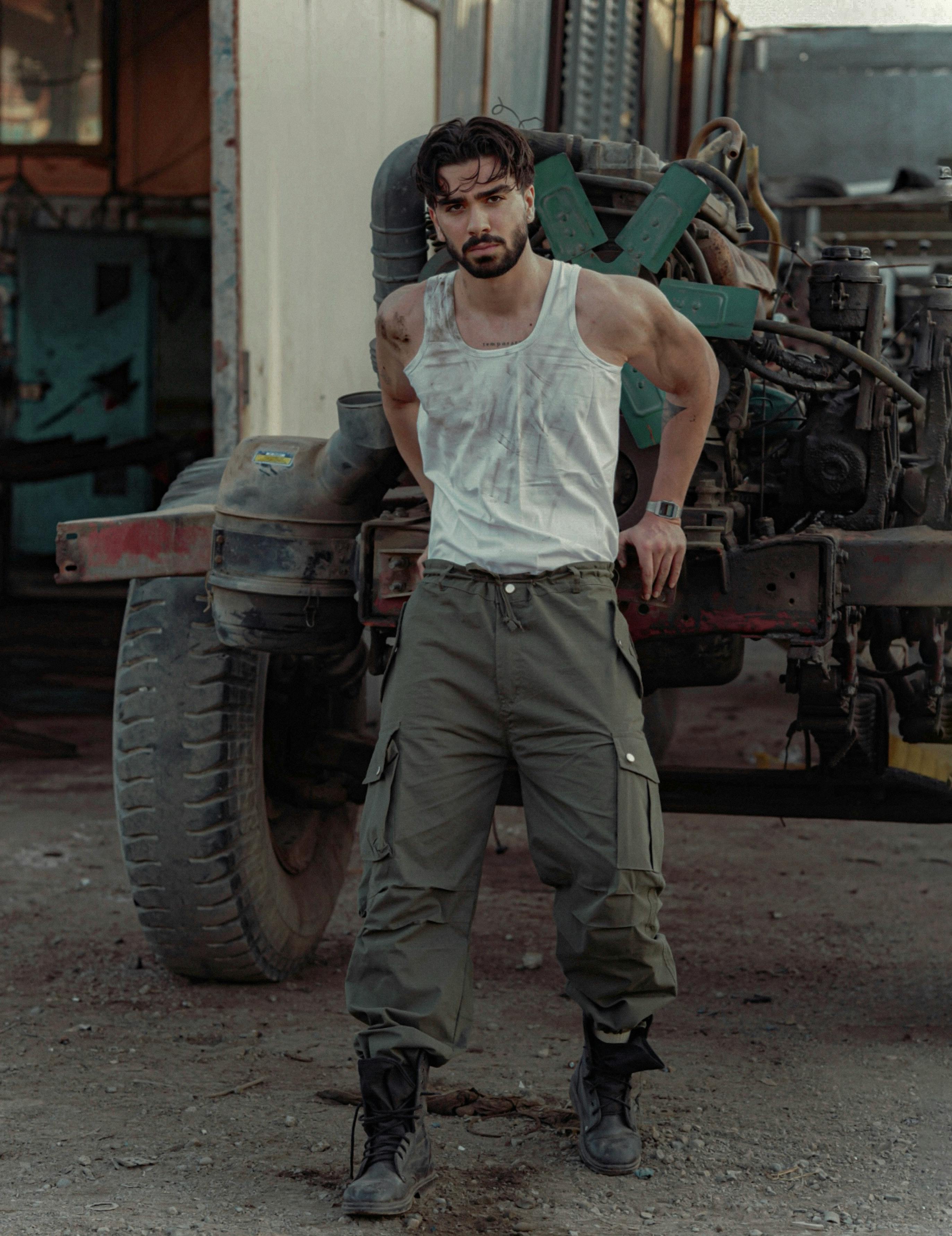 Bearded Man in a Dirty Tank Top Standing next to a Broken Vehicle ...