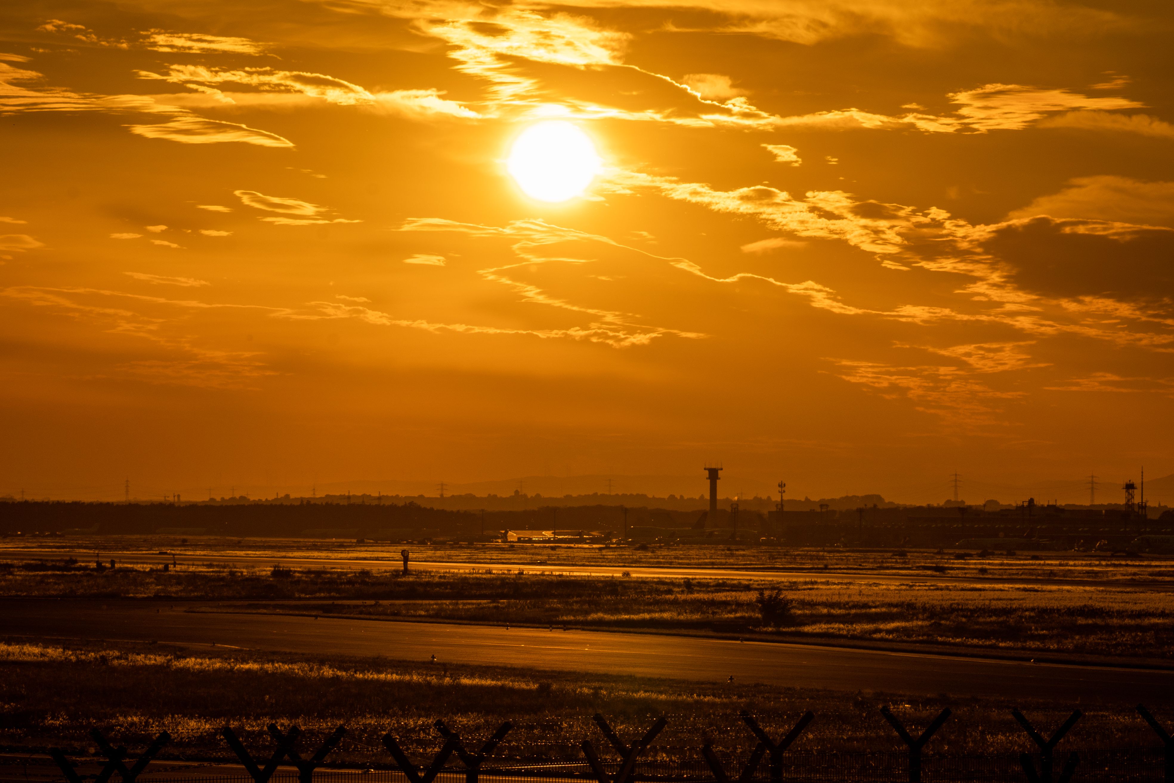 A sunset over an airport runway with a fence · Free Stock Photo