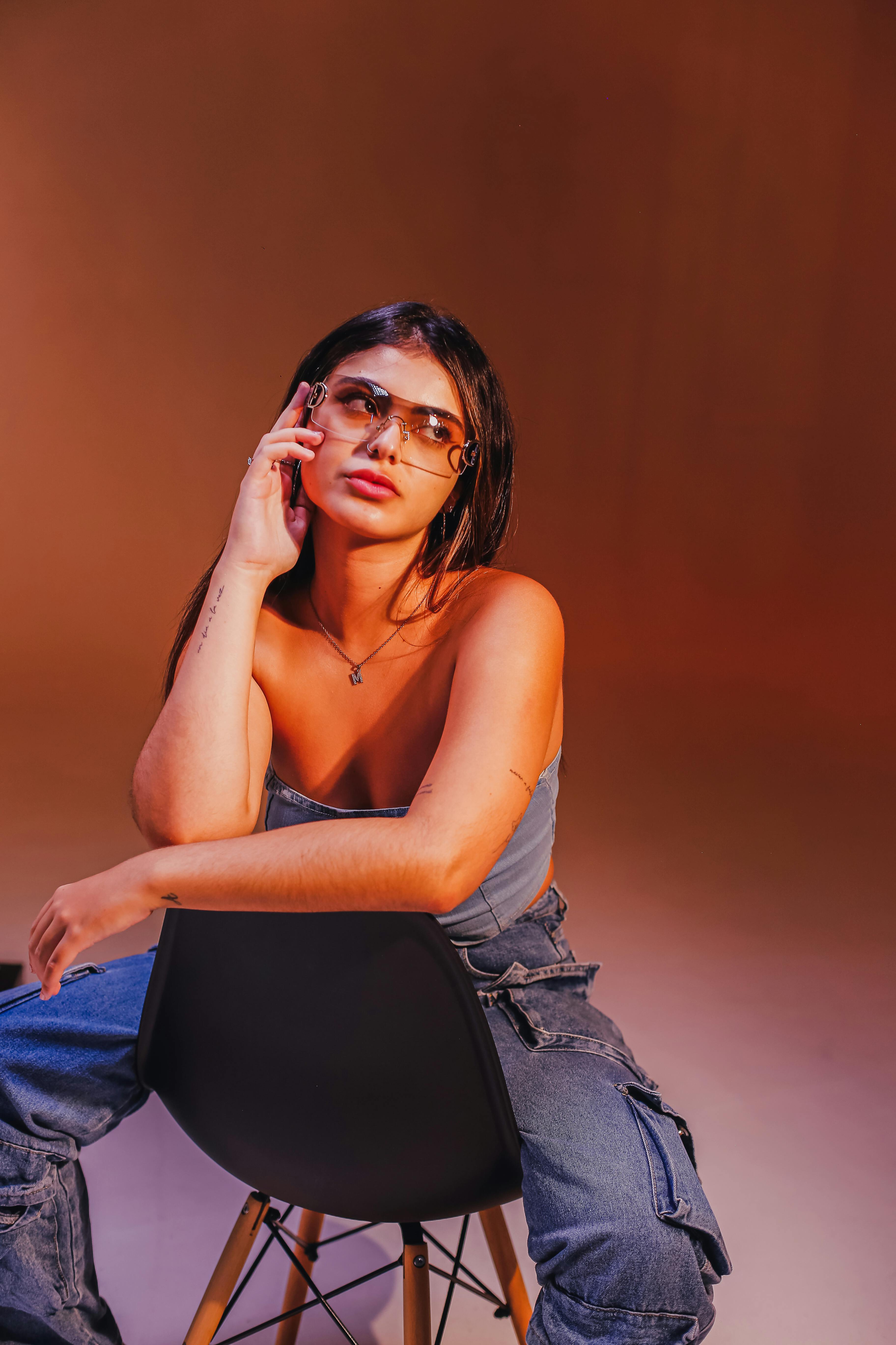 A woman in jeans and glasses sitting on a chair · Free Stock Photo