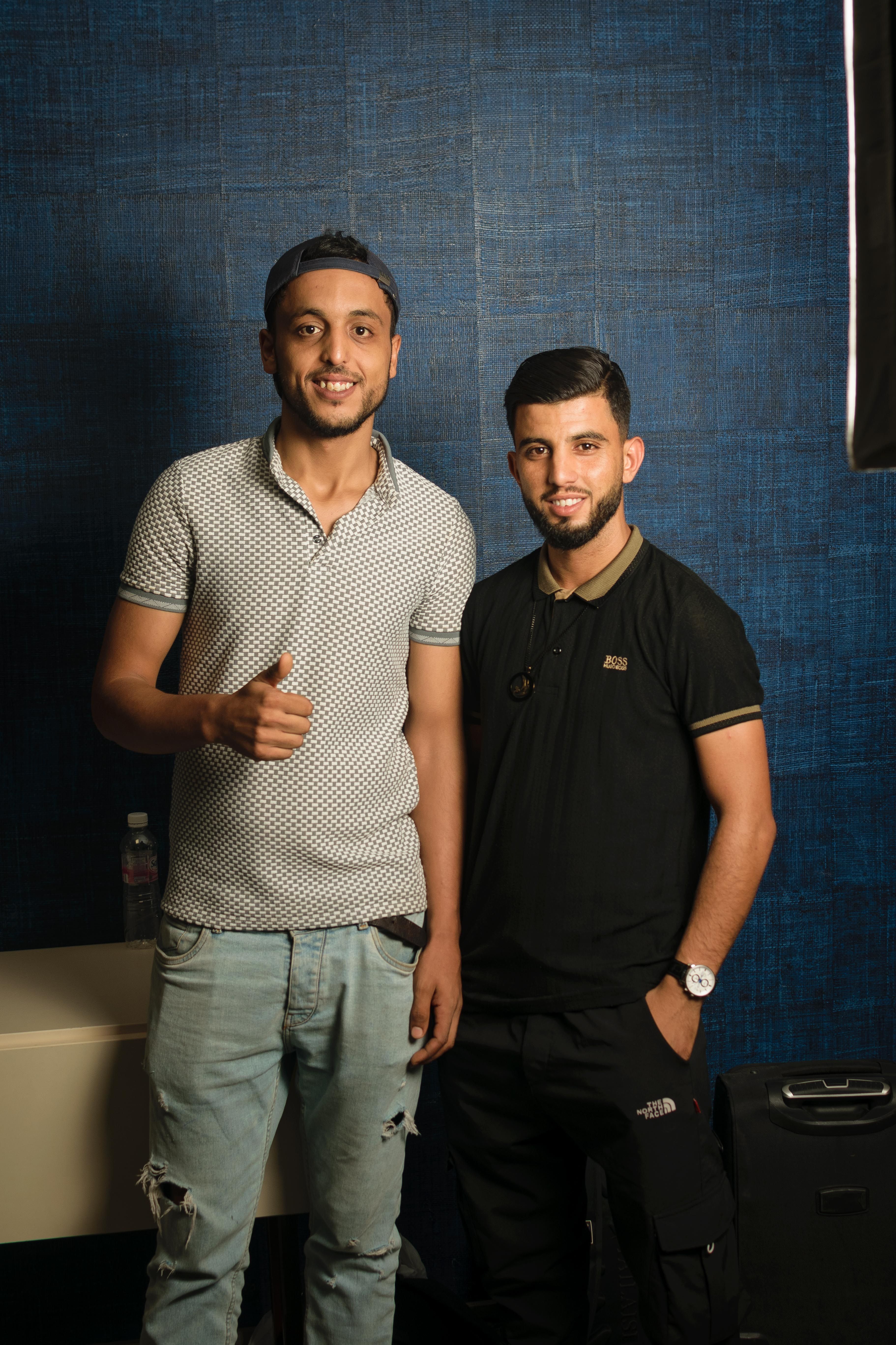 Two Men in Casual Outfits Standing against a Blue Wall · Free Stock Photo