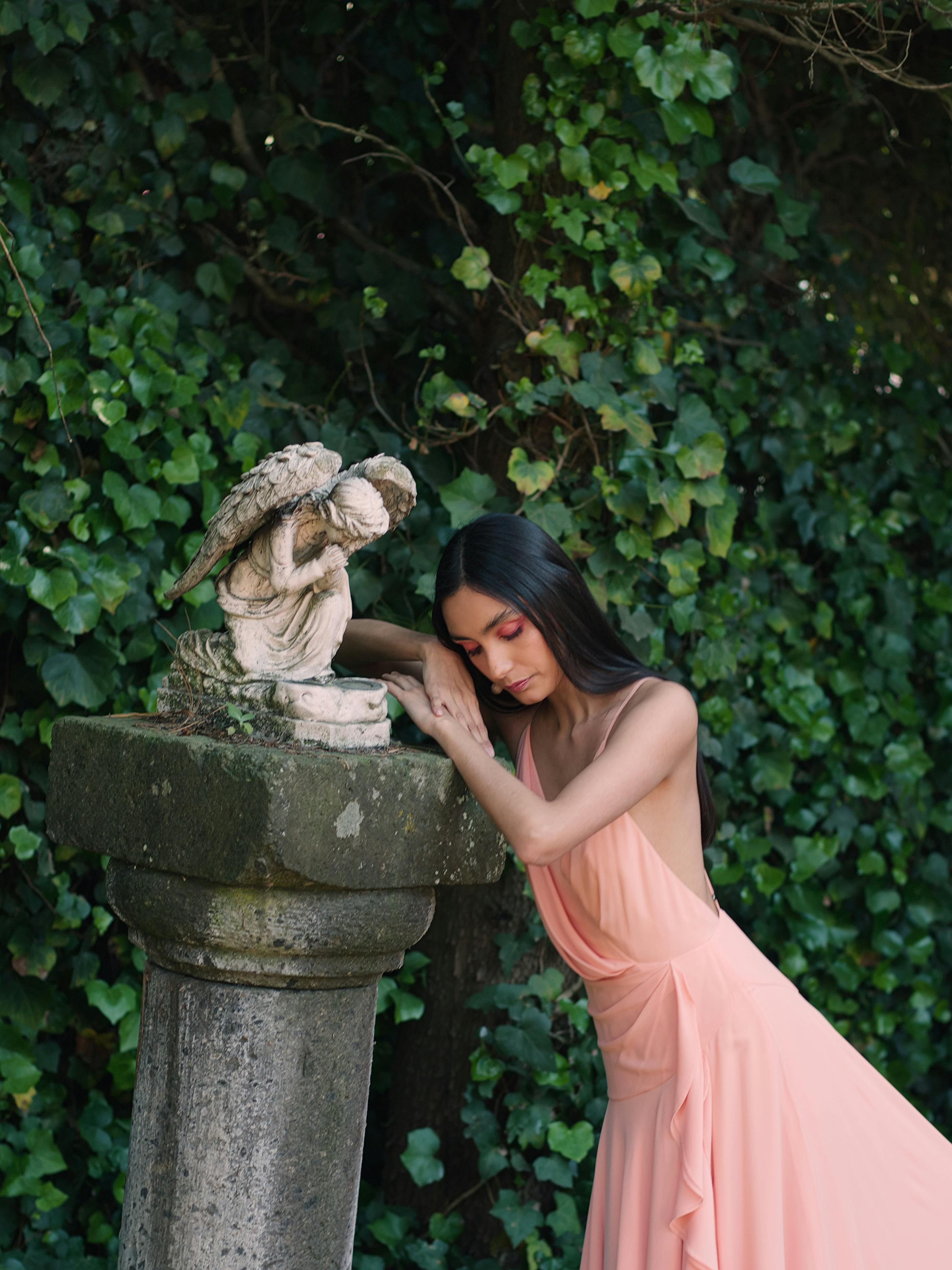 Woman in Pink Dress Leaning on Angel Sculpture · Free Stock Photo