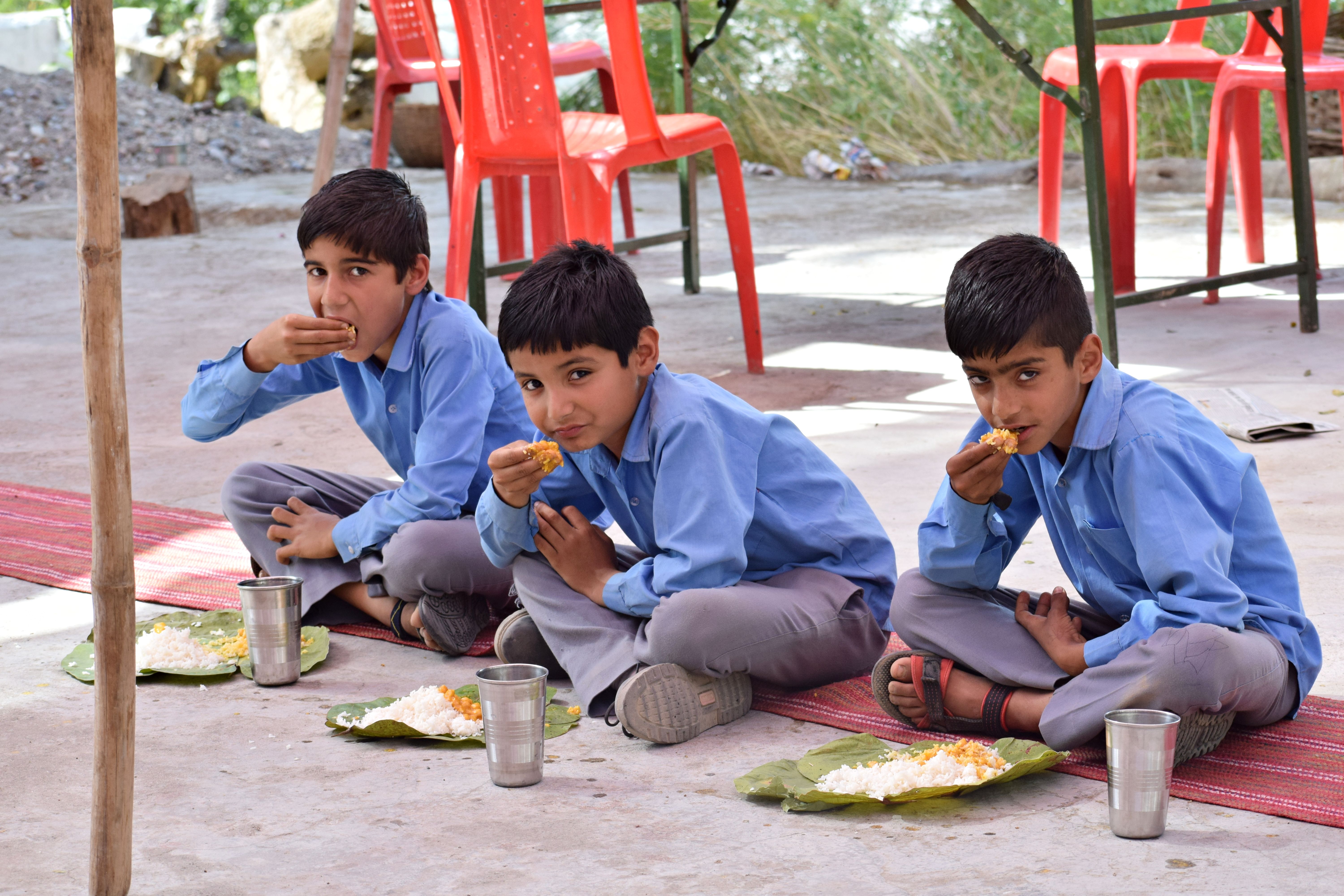 Three boys sitting on the ground eating food · Free Stock Photo