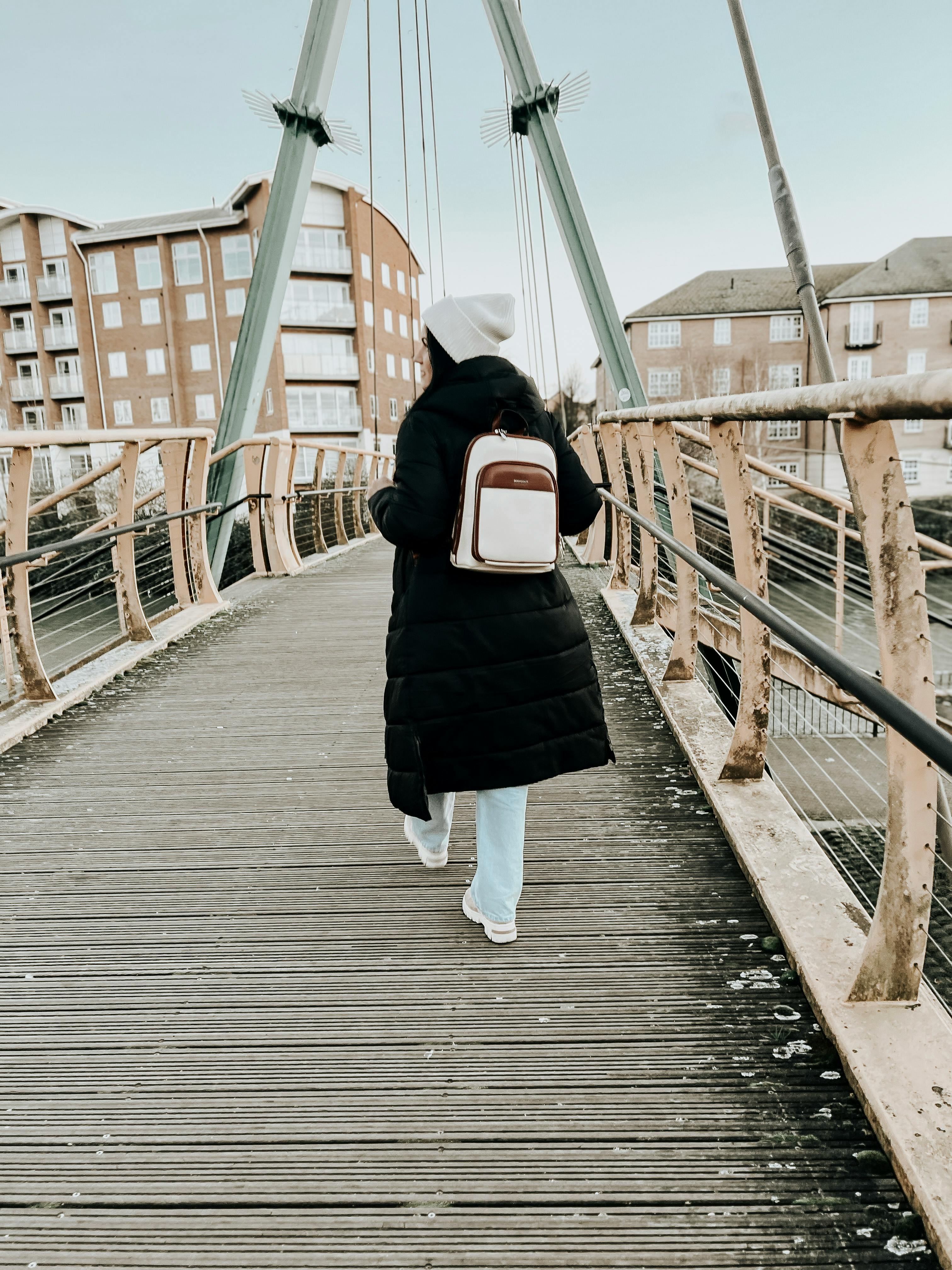 Woman in Coat and with Backpack on Footbridge in City · Free Stock Photo