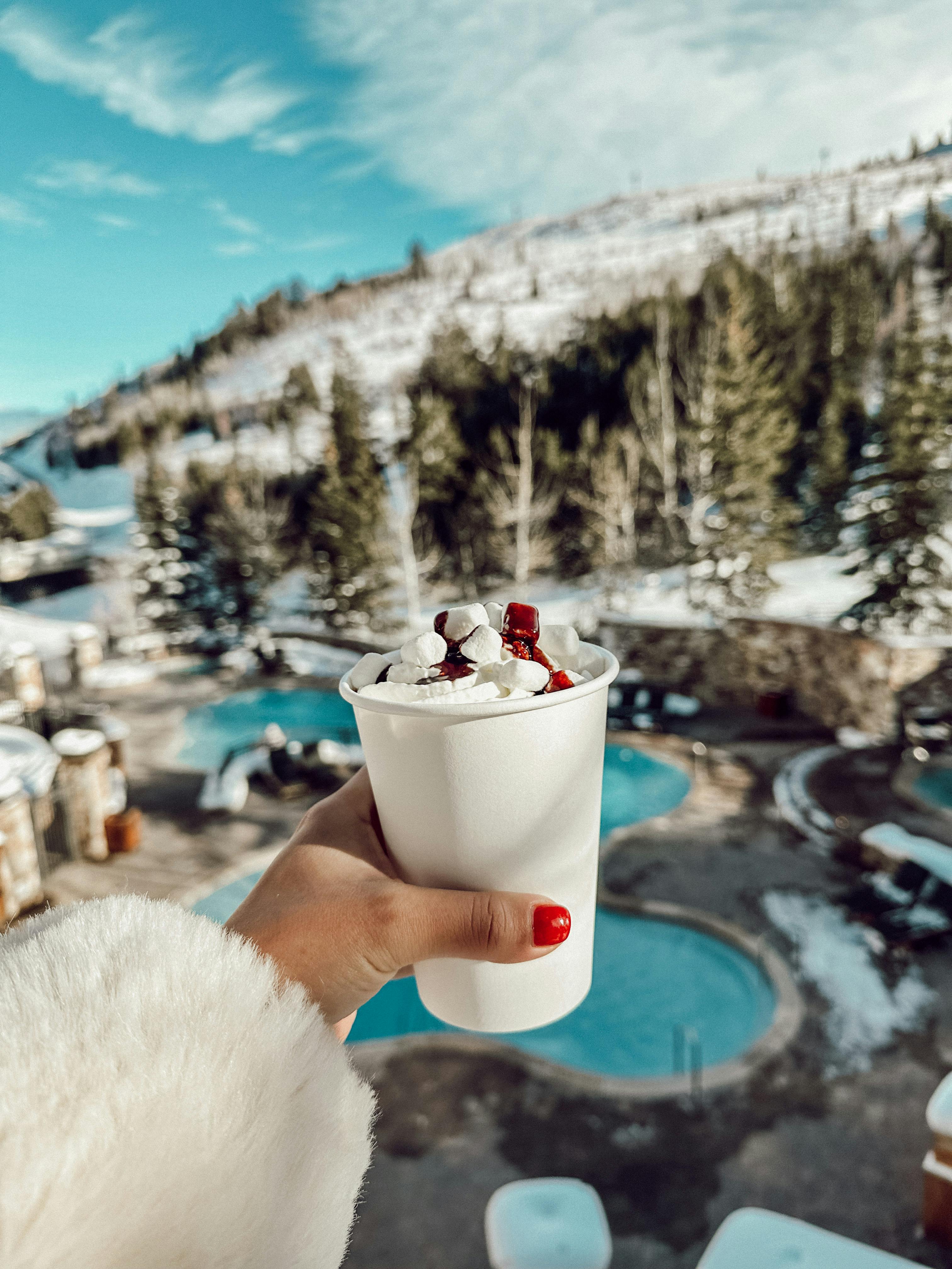 A person holding a cup of hot chocolate in front of a pool · Free Stock ...