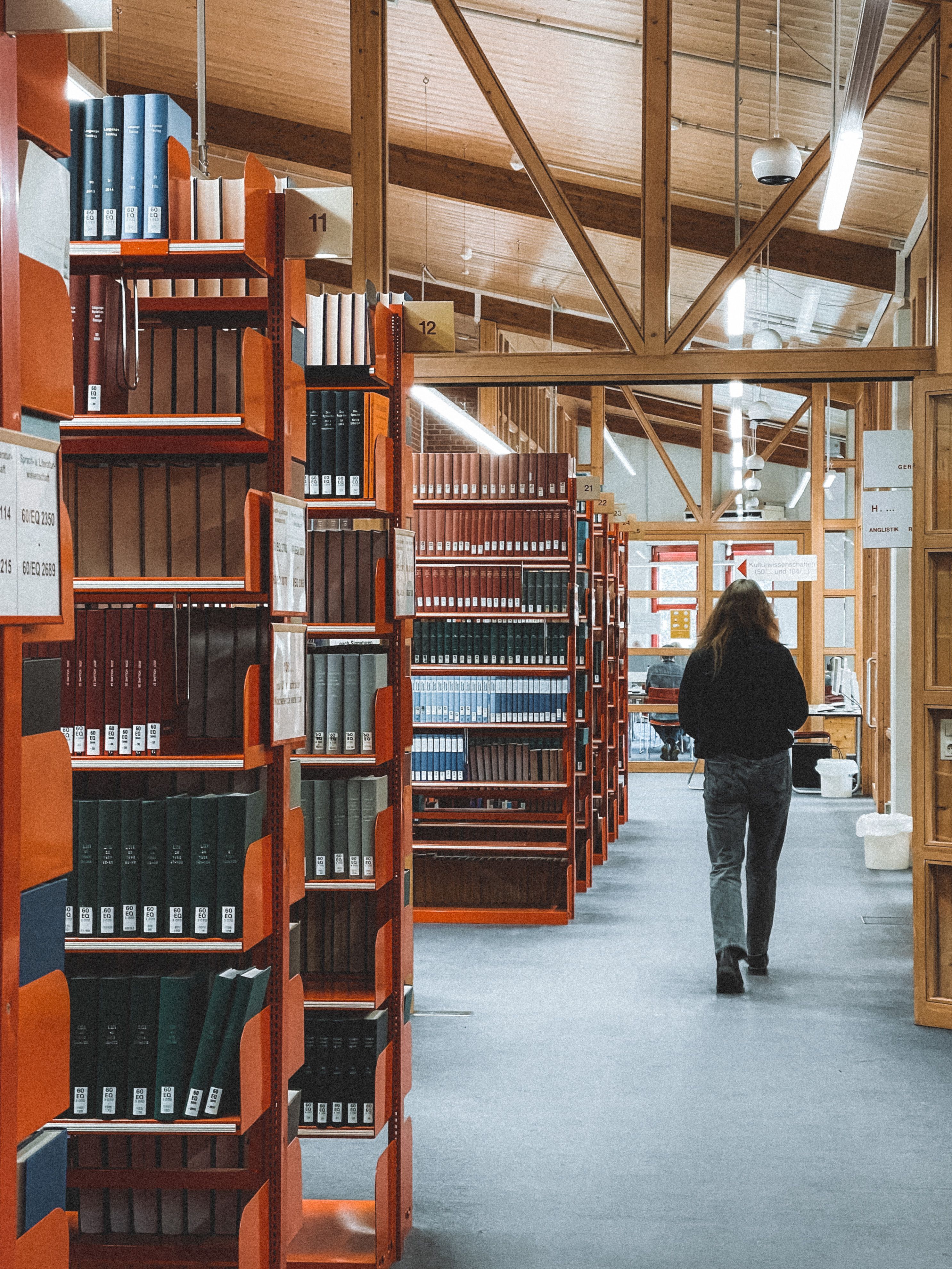 A woman walking through a library with bookshelves · Free Stock Photo