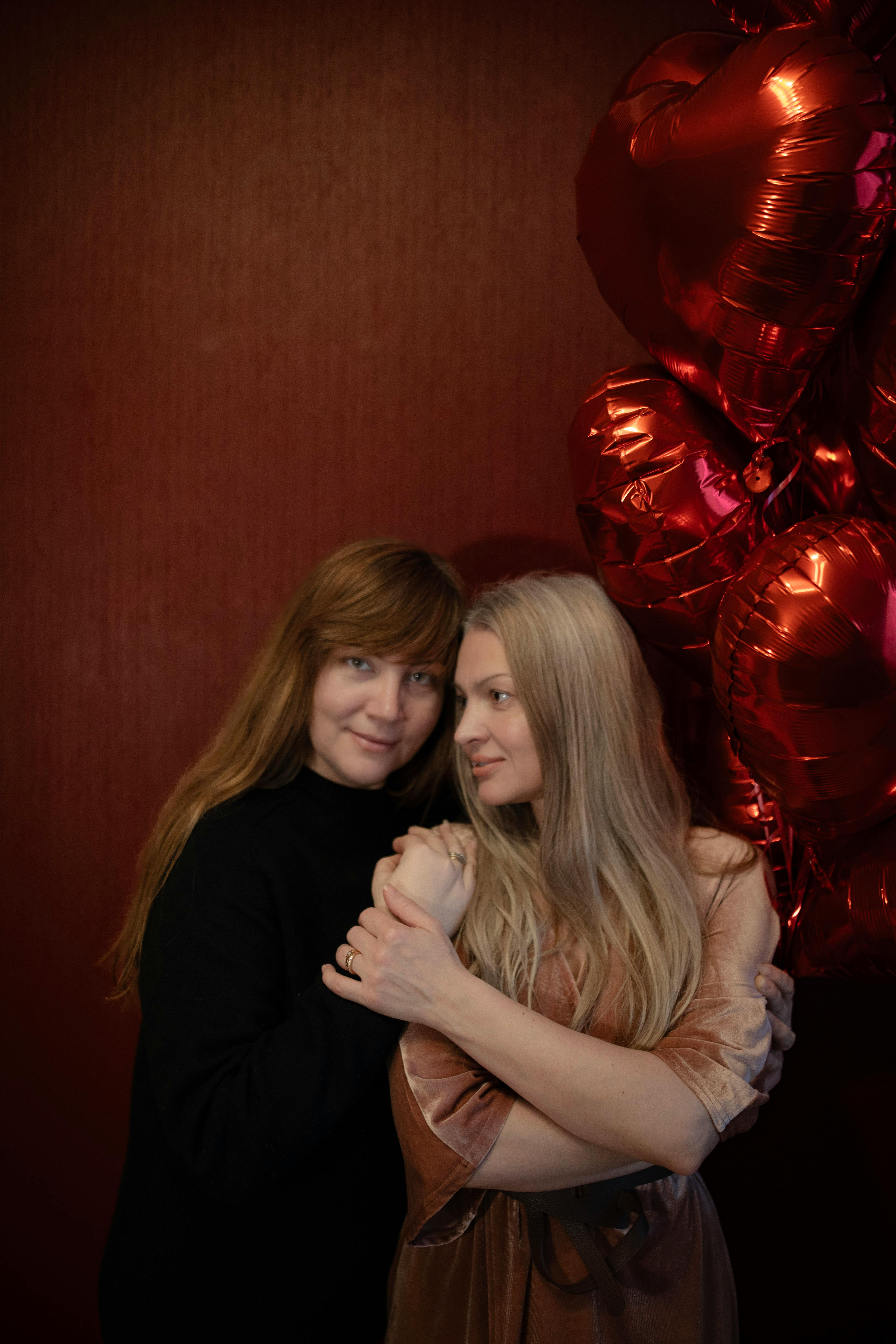 Two women hugging in front of a red wall with red balloons · Free Stock ...