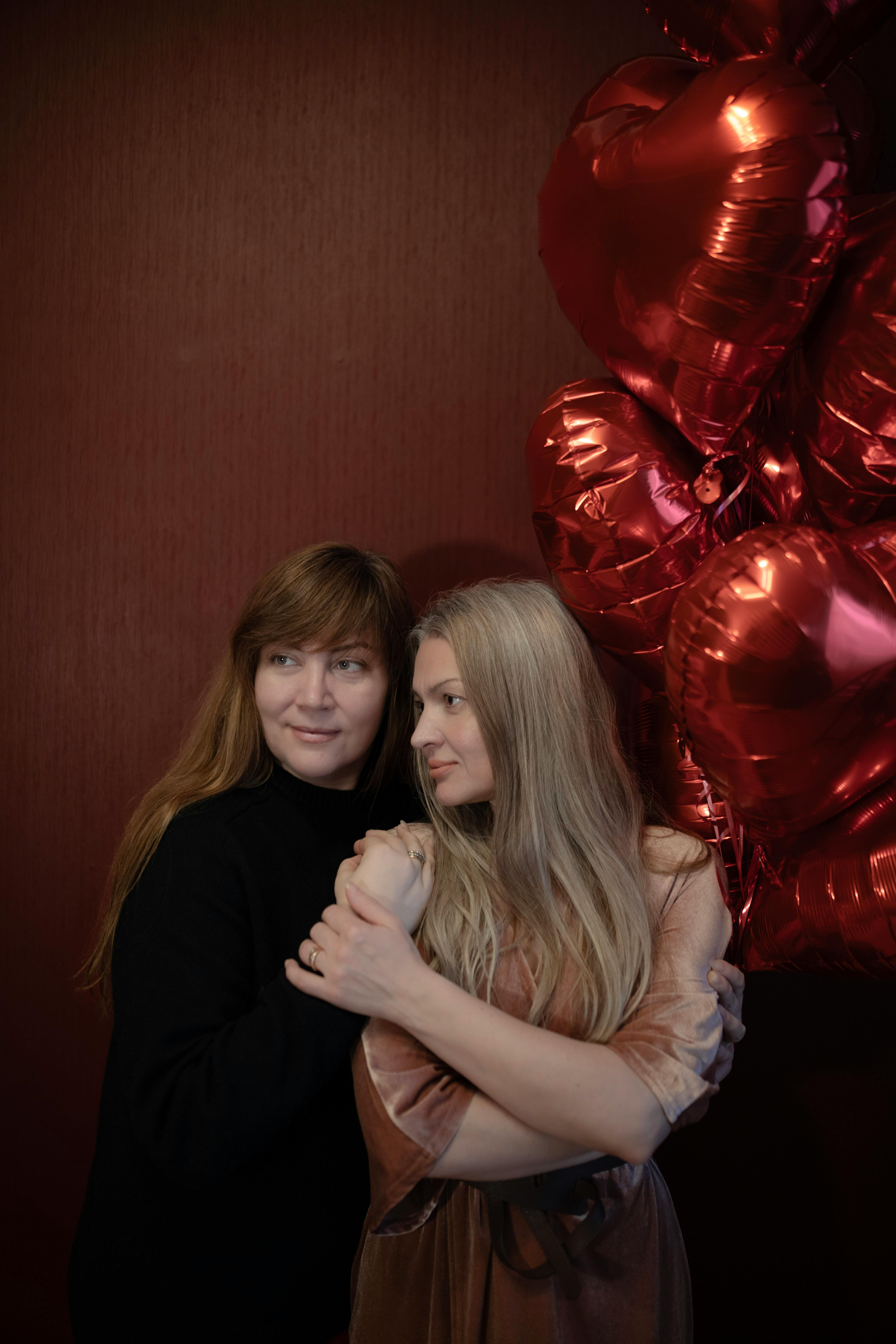 Two women hugging in front of red heart balloons · Free Stock Photo