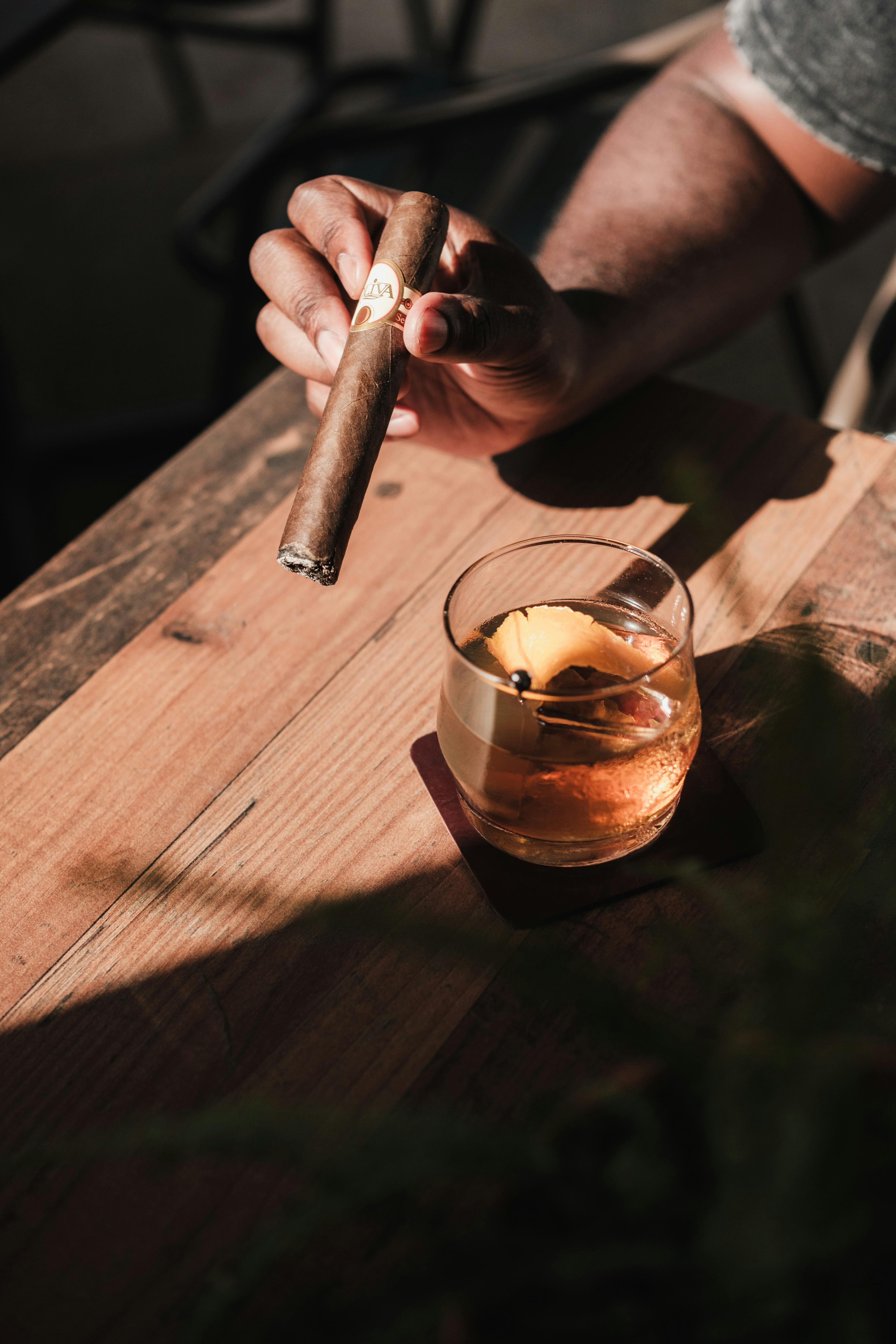 Man Holding a Puro Cigar near the Cocktail · Free Stock Photo