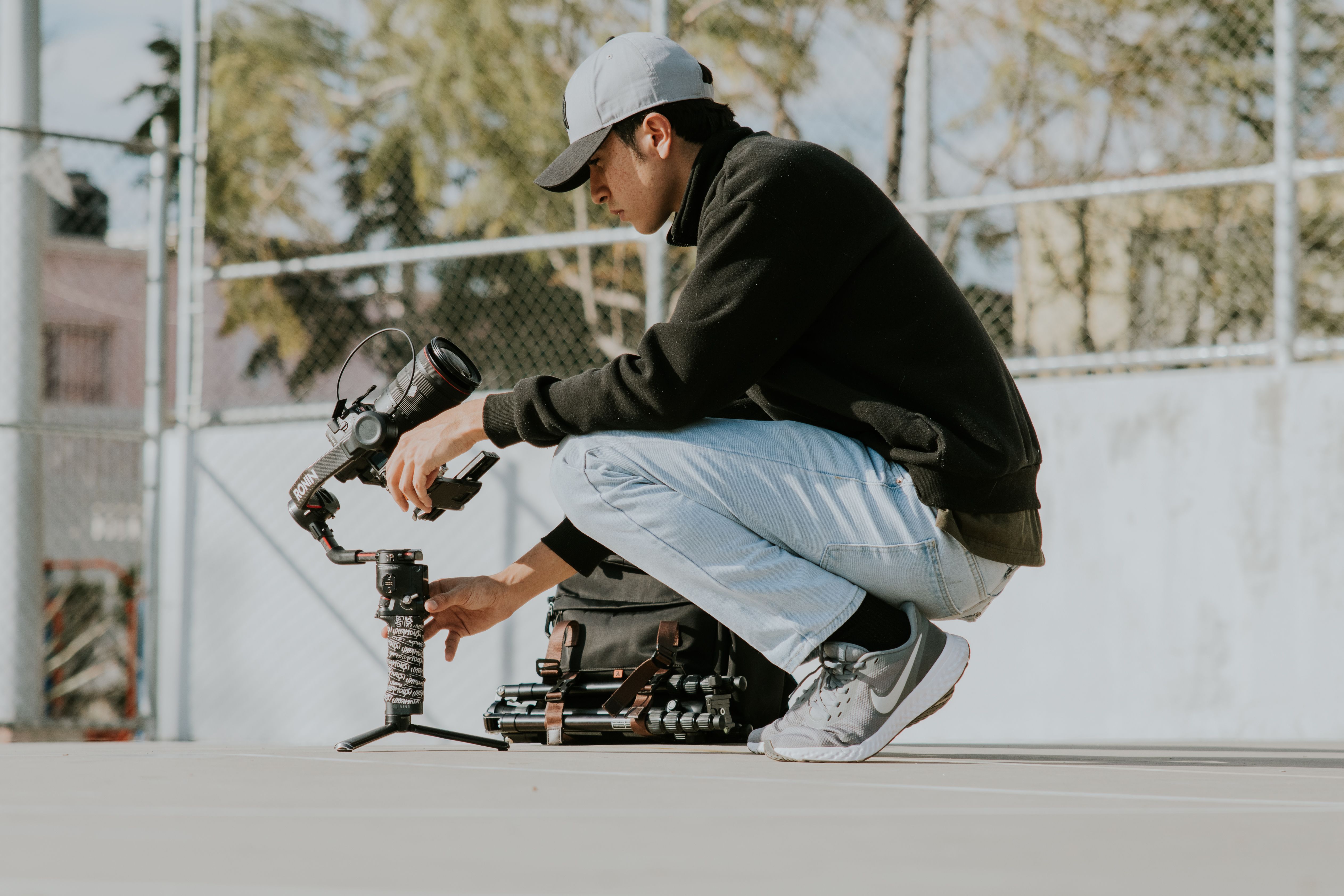 Man in Cap Squatting and Holding Camera · Free Stock Photo
