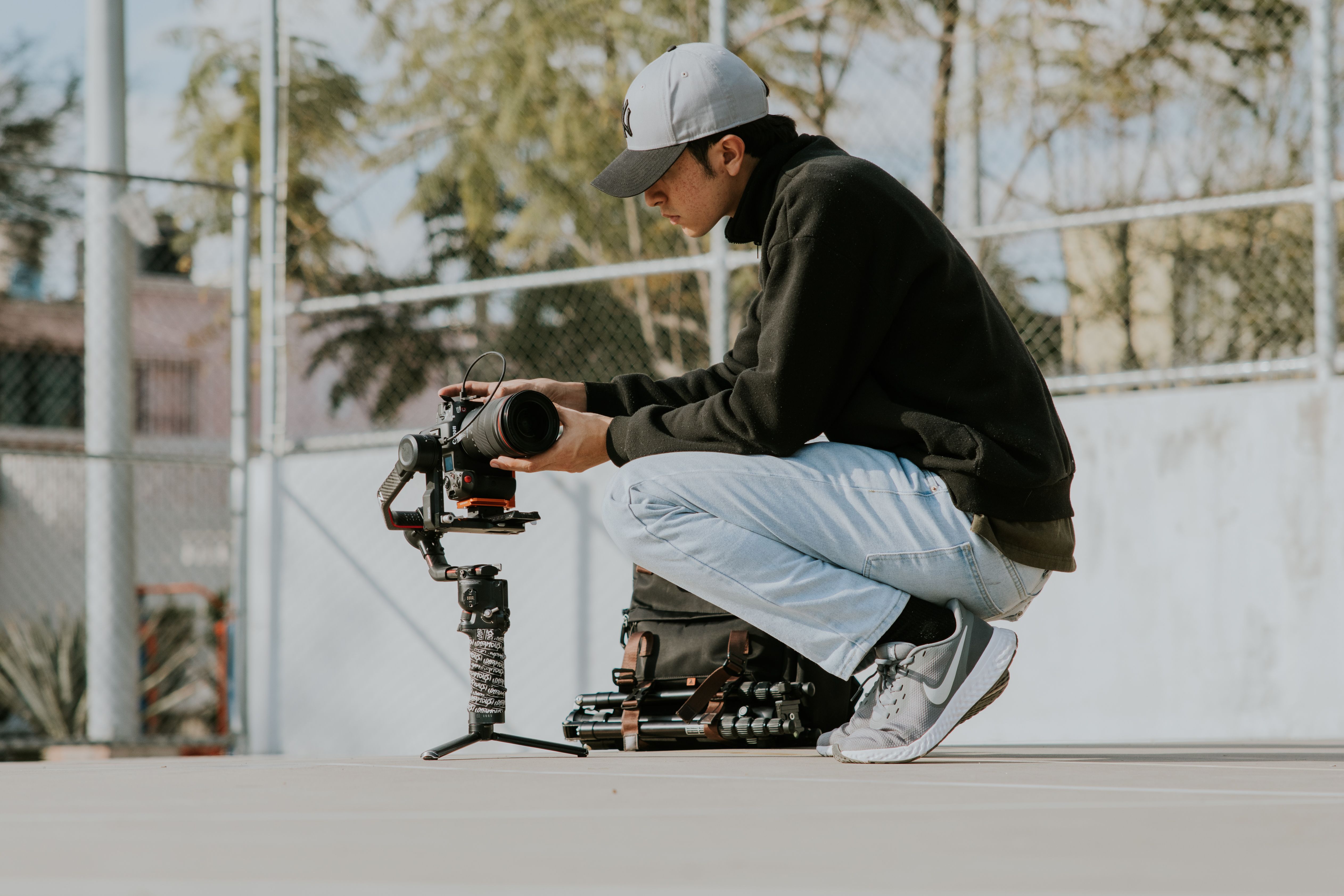 Man in Cap Squatting with Camera · Free Stock Photo