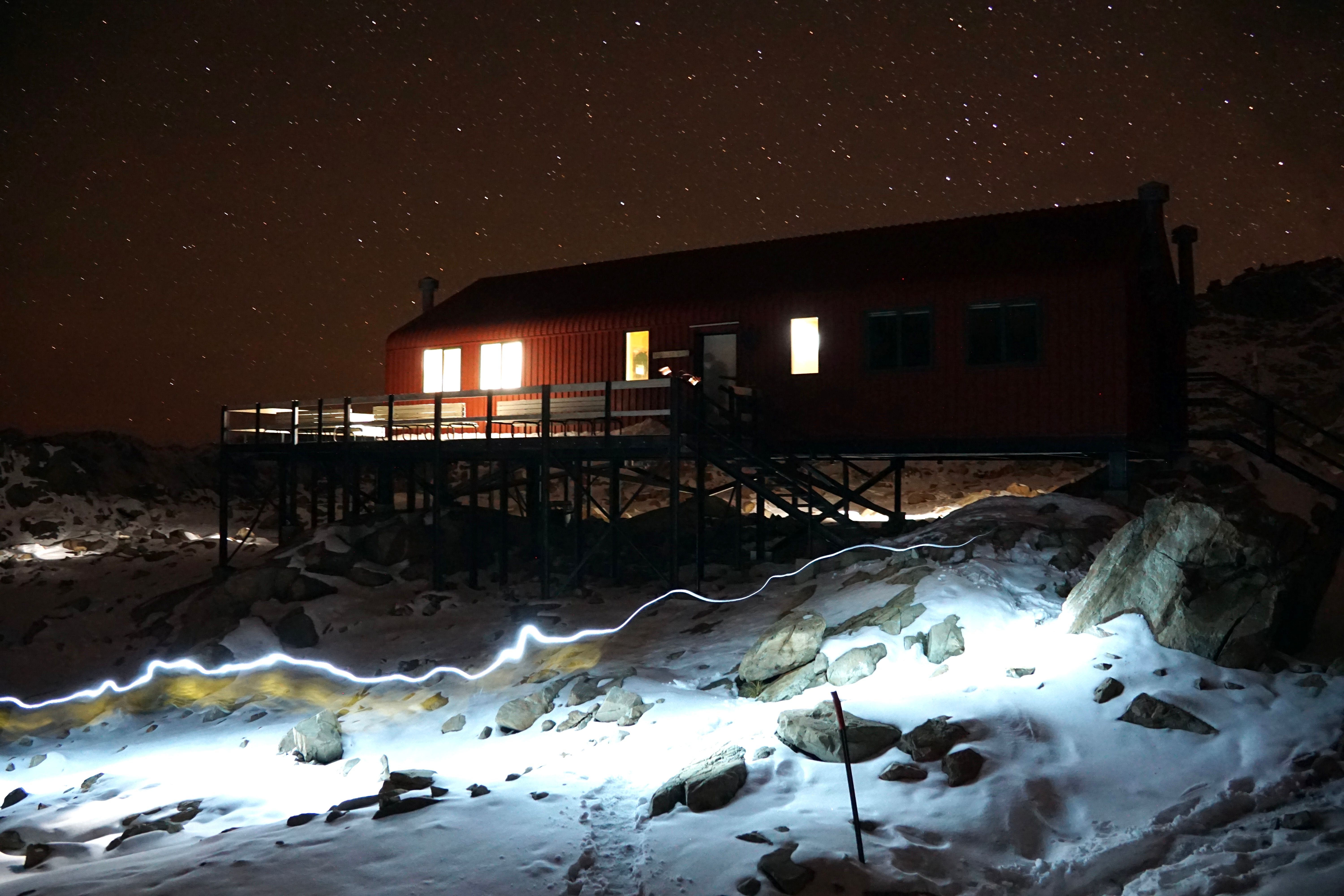 A cabin is lit up at night with snow on the ground · Free Stock Photo