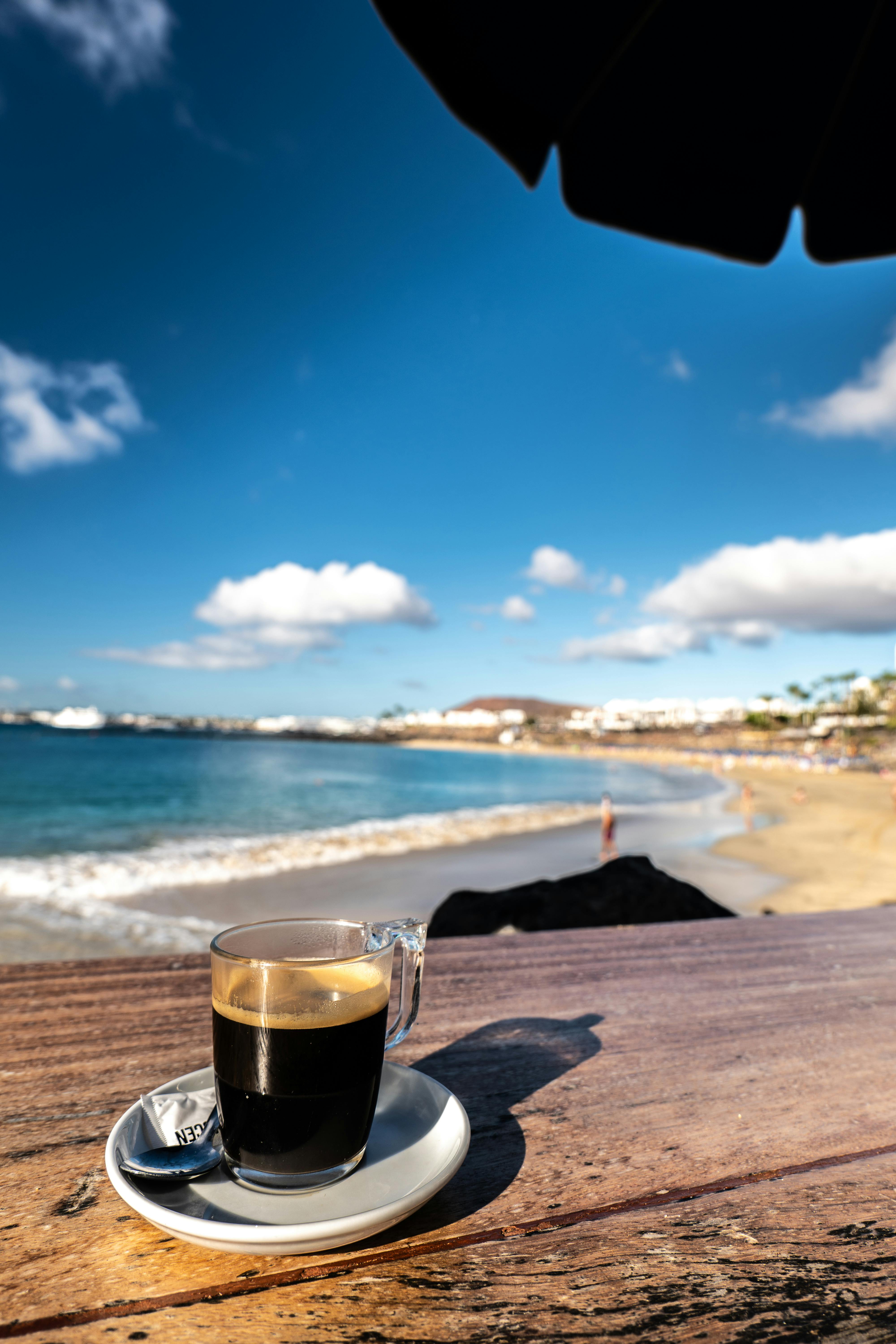 Coffee on Sunlit Table on Beach · Free Stock Photo