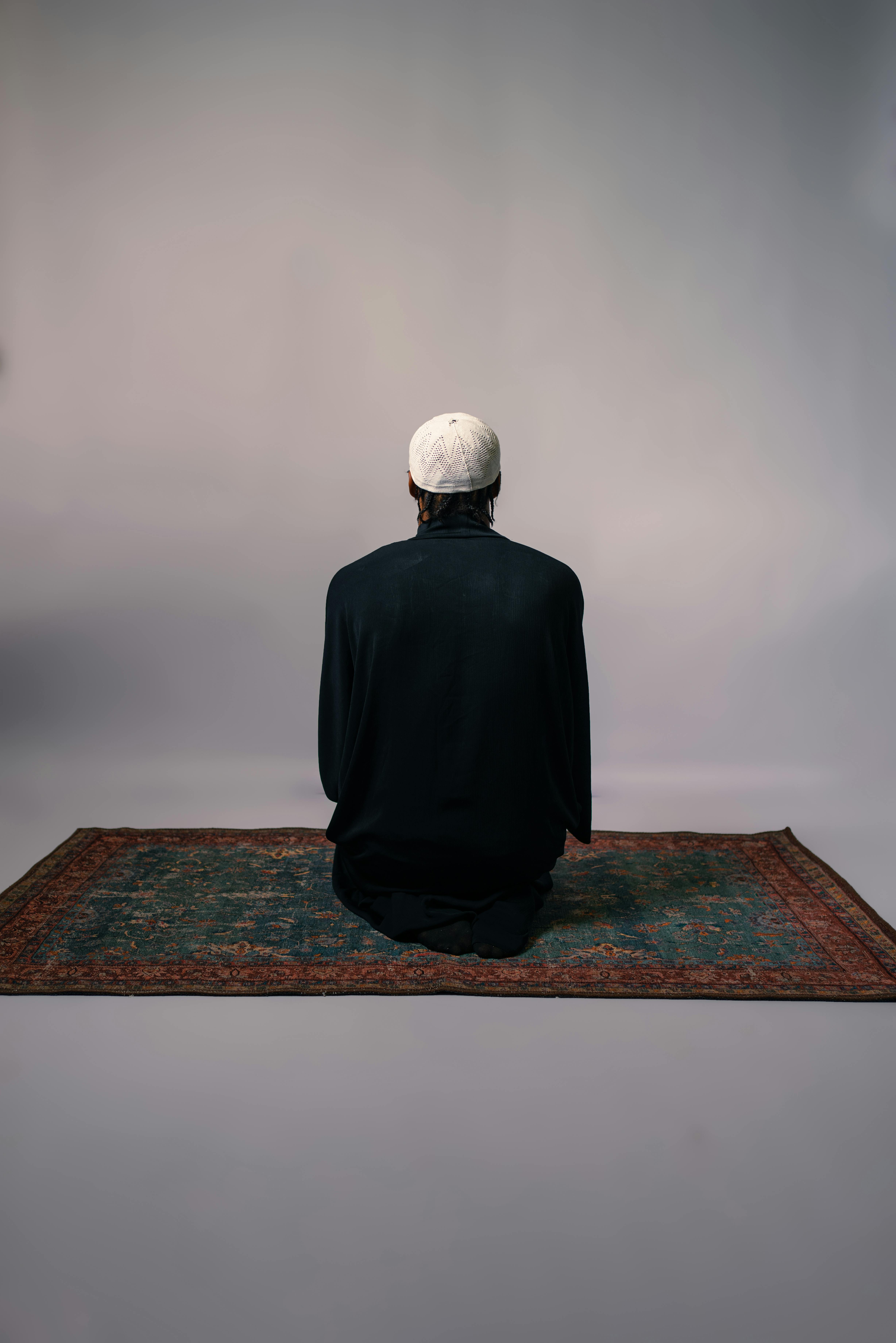 Back View of a Man Sitting on a Rug and Praying · Free Stock Photo