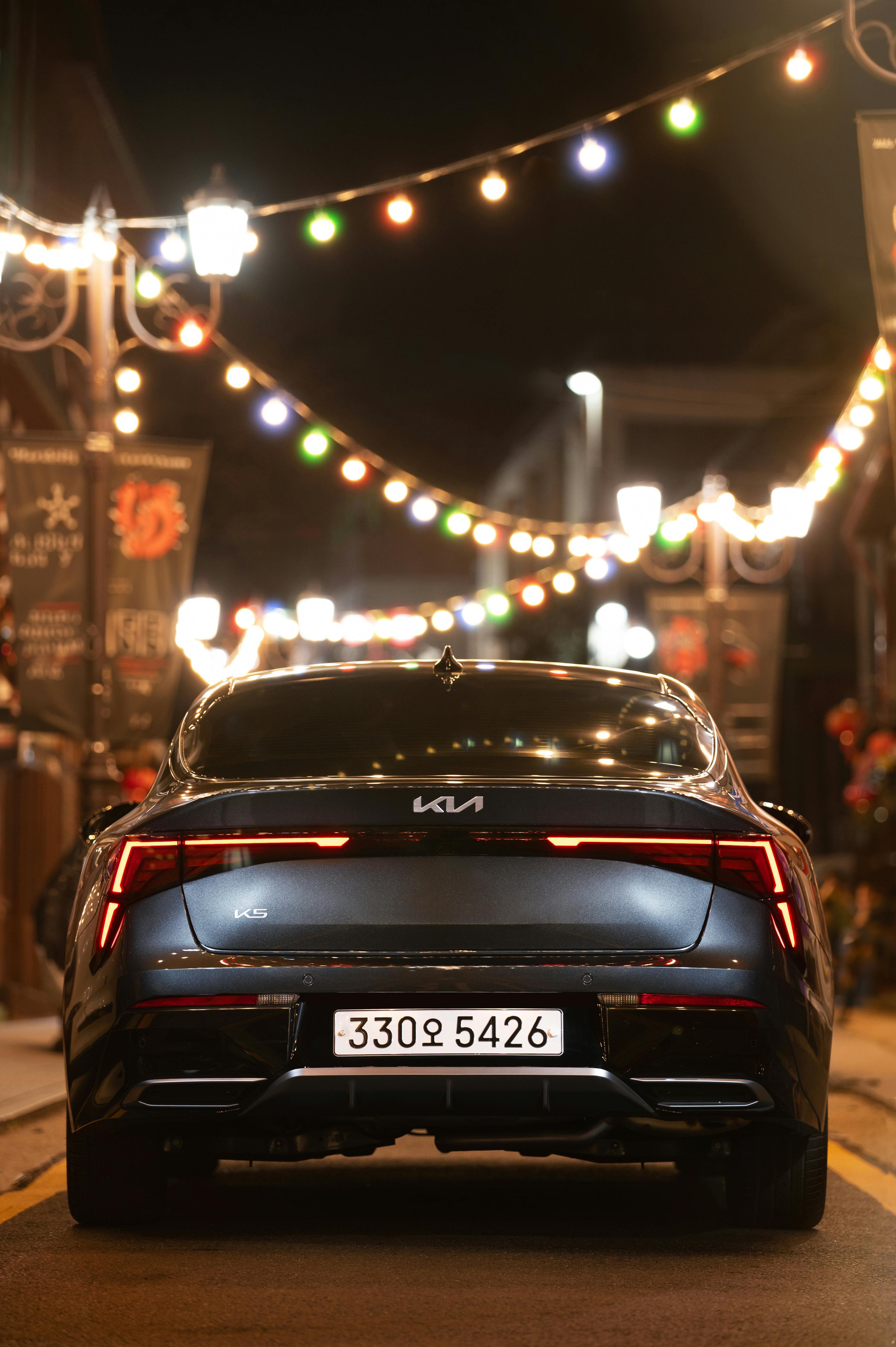 The rear view of the Kia K5 on a road full of bright Christmas lights ...