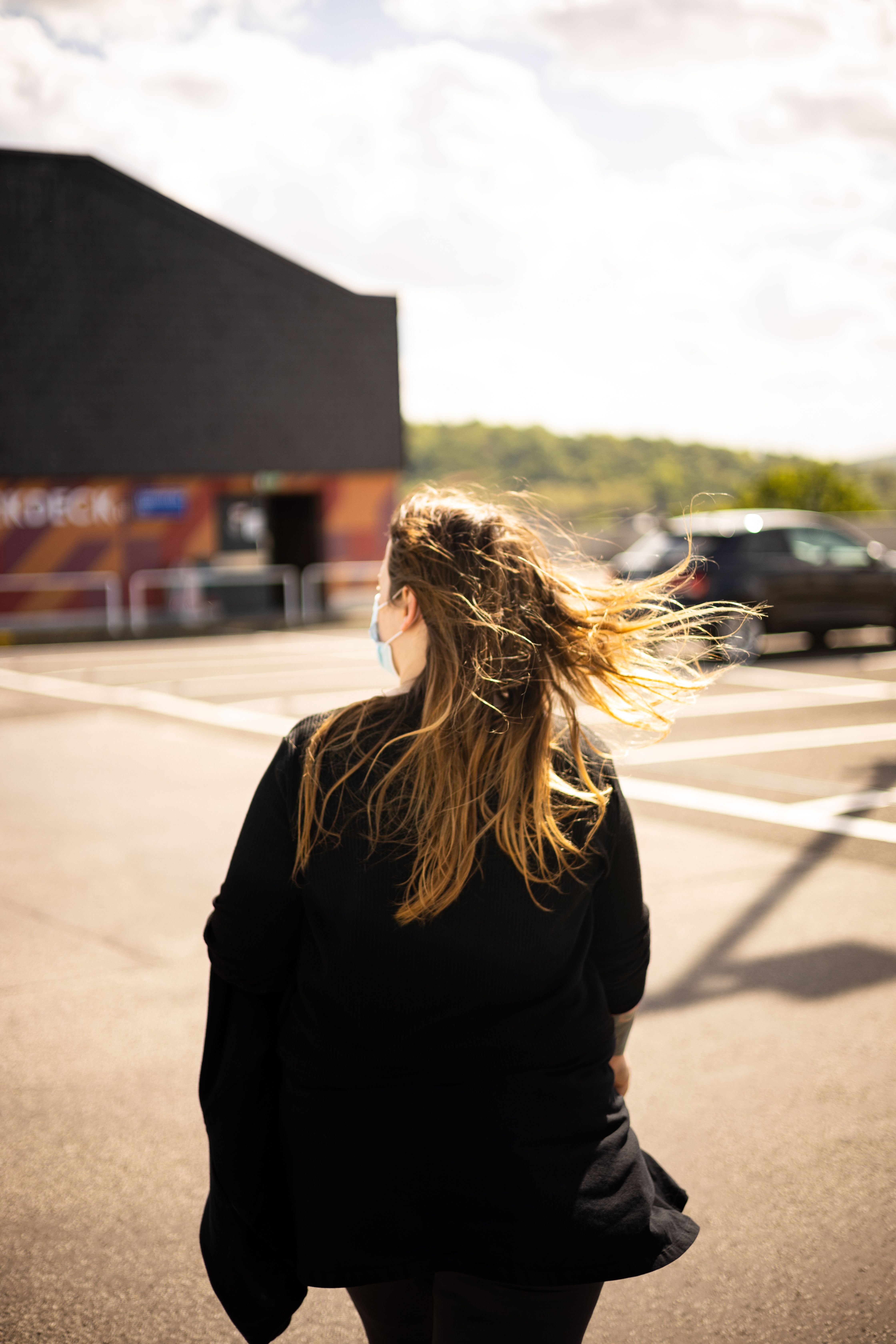 Back View of a Woman Walking through a Parking Lot on a Windy Day ...