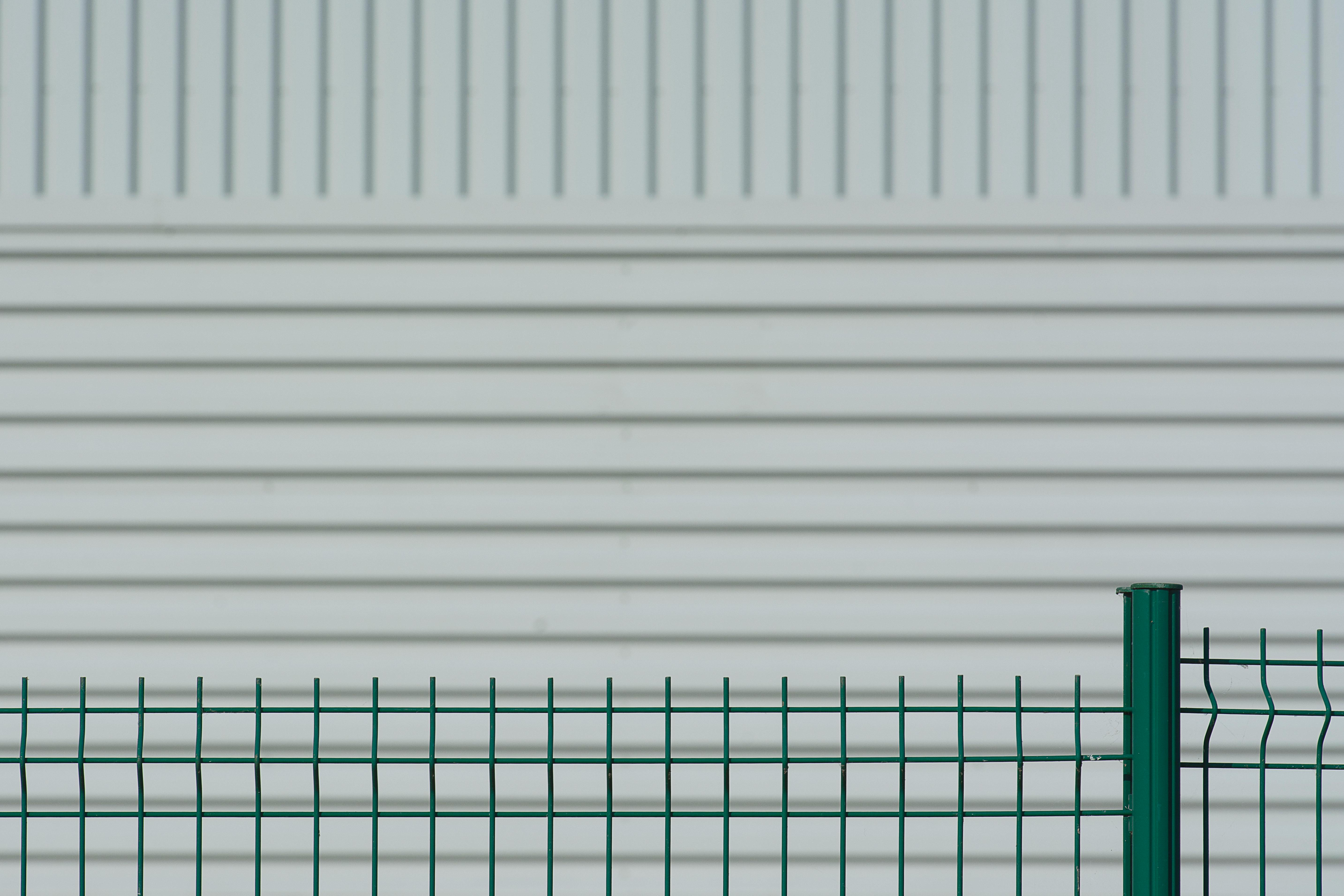 A green and white fence with a green metal bar · Free Stock Photo