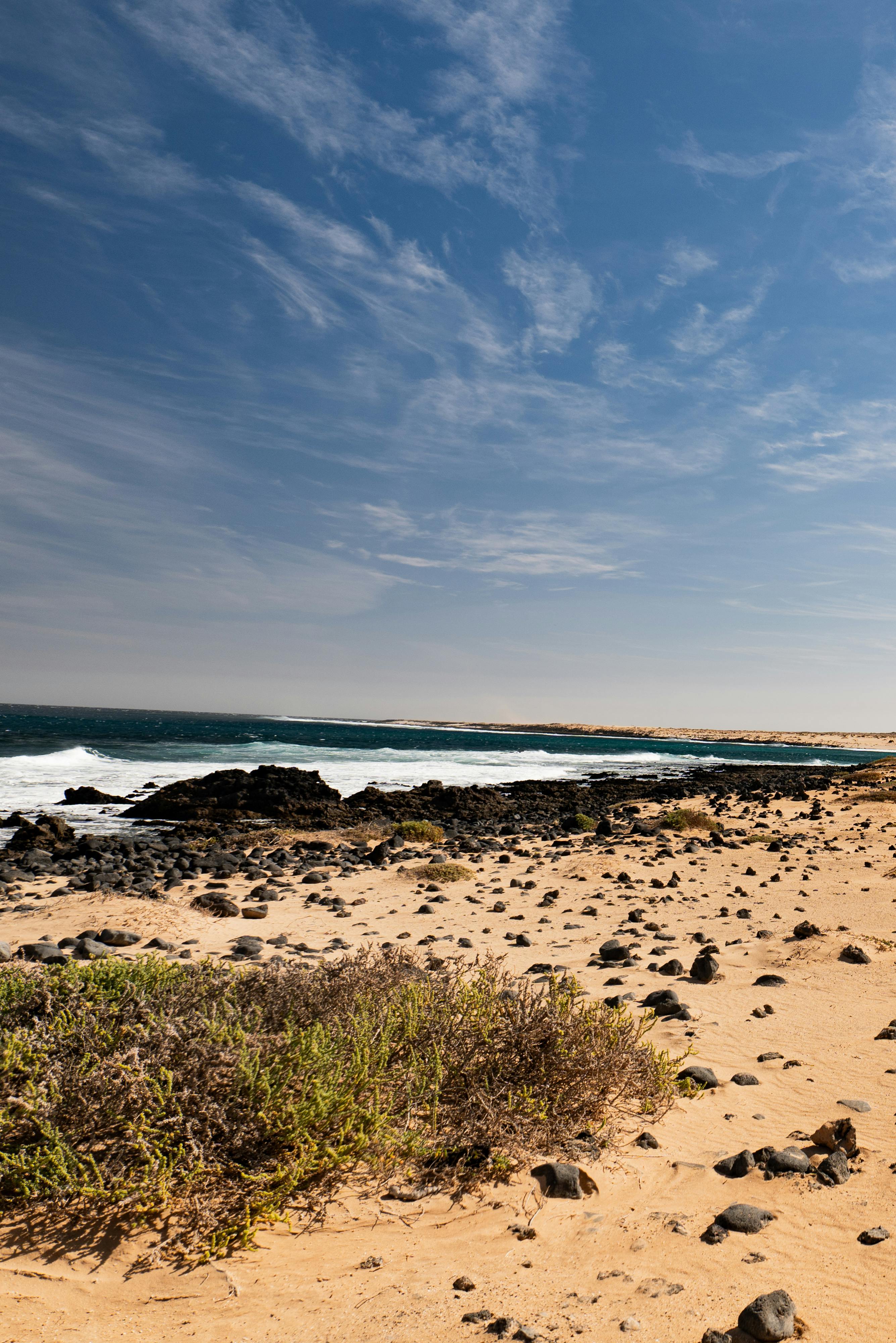A sandy beach with rocks and a blue sky · Free Stock Photo