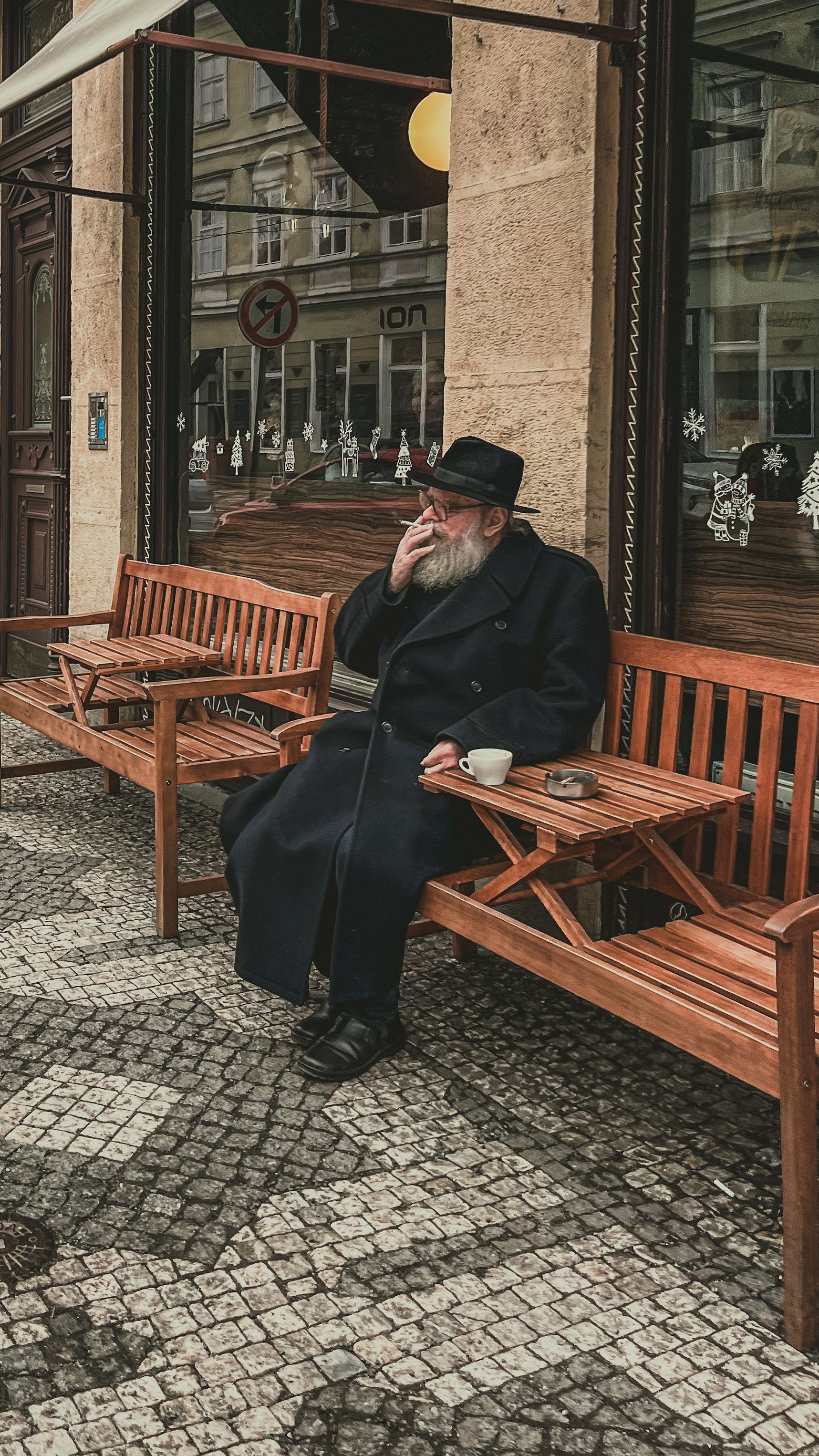 Bearded Man in a Black Coat and Hat Smoking a Cigarette on a Bench in ...