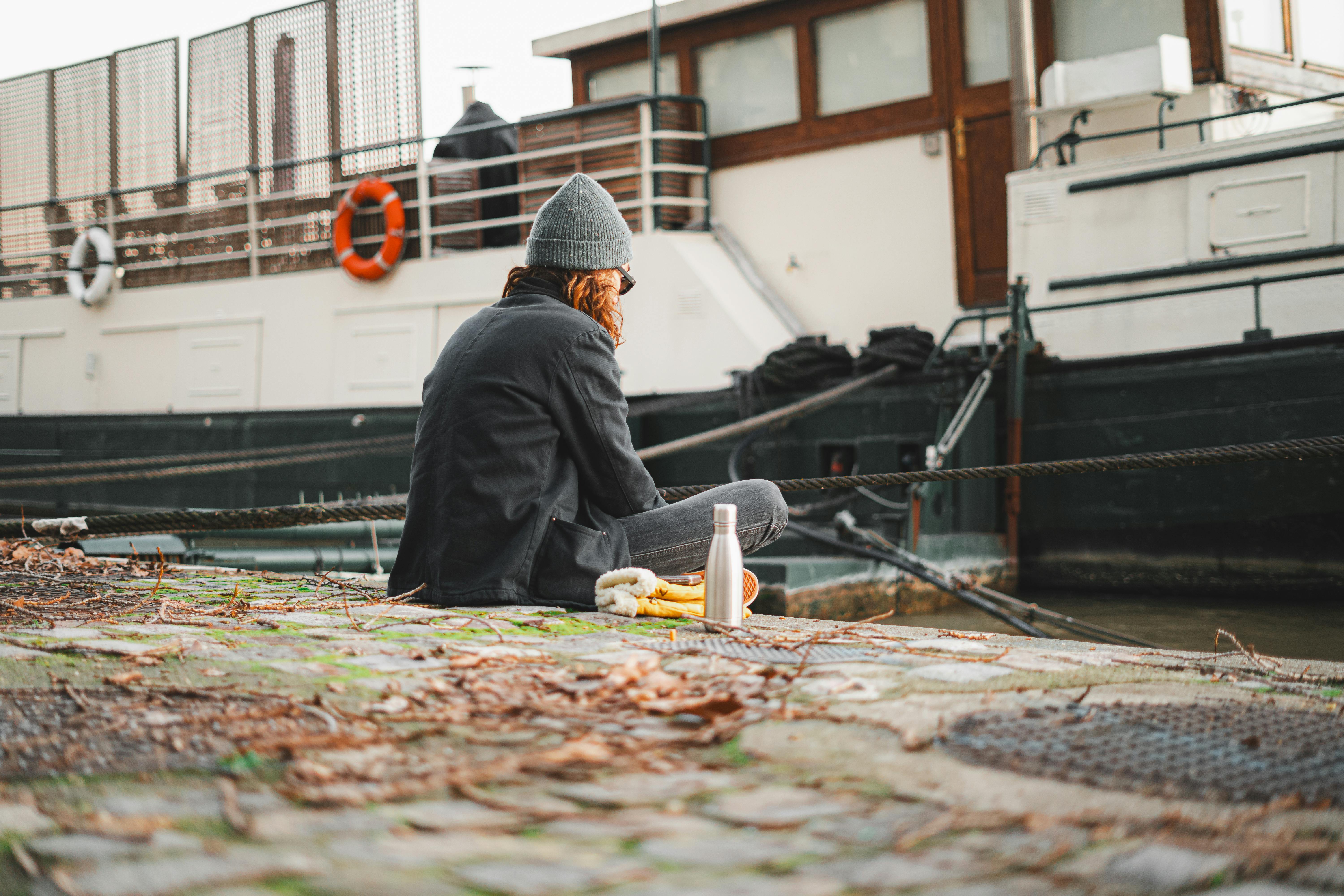 A man sitting on a dock next to a boat · Free Stock Photo