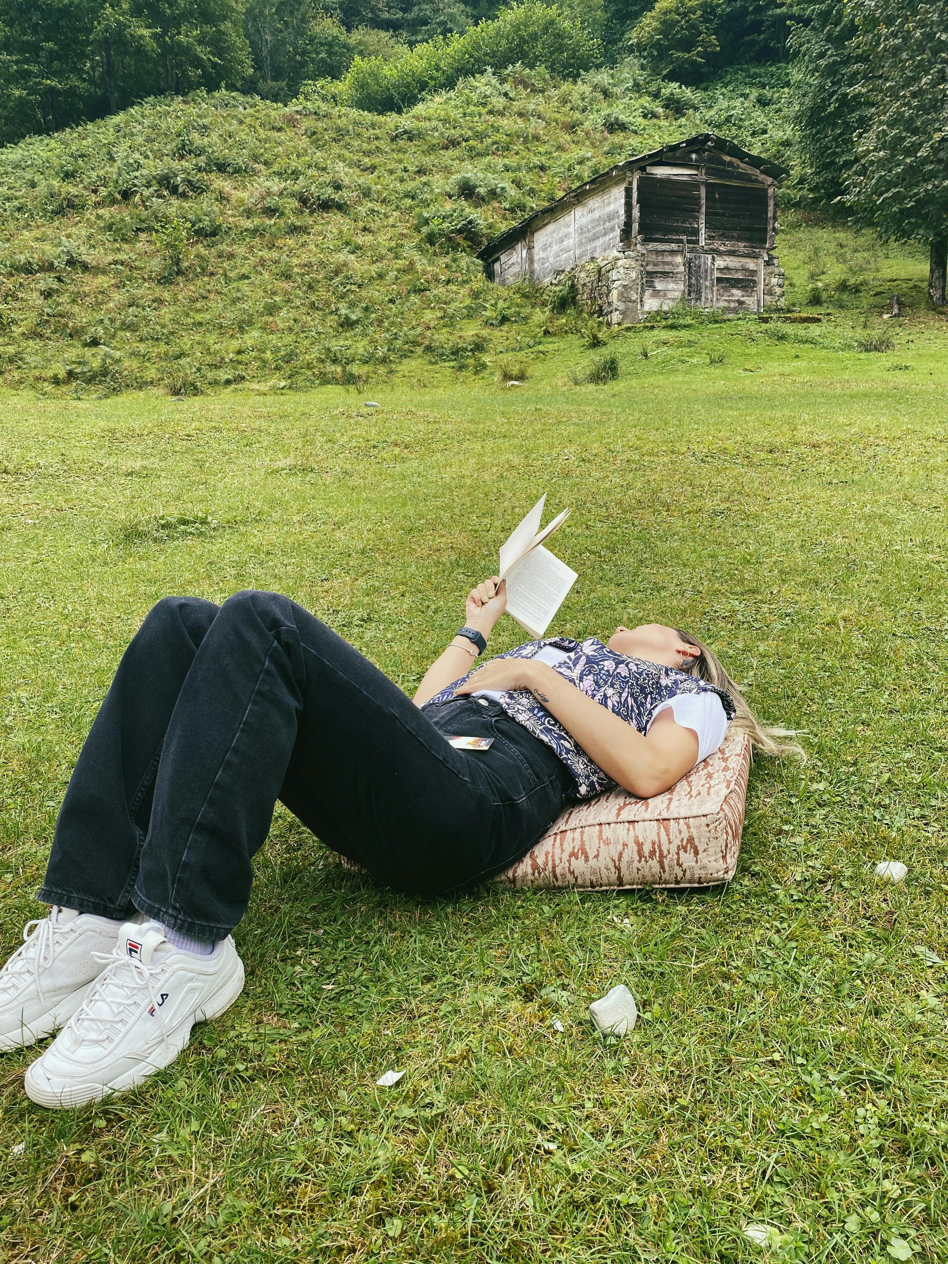 A Woman Lying on a Meadow and Reading a Book · Free Stock Photo