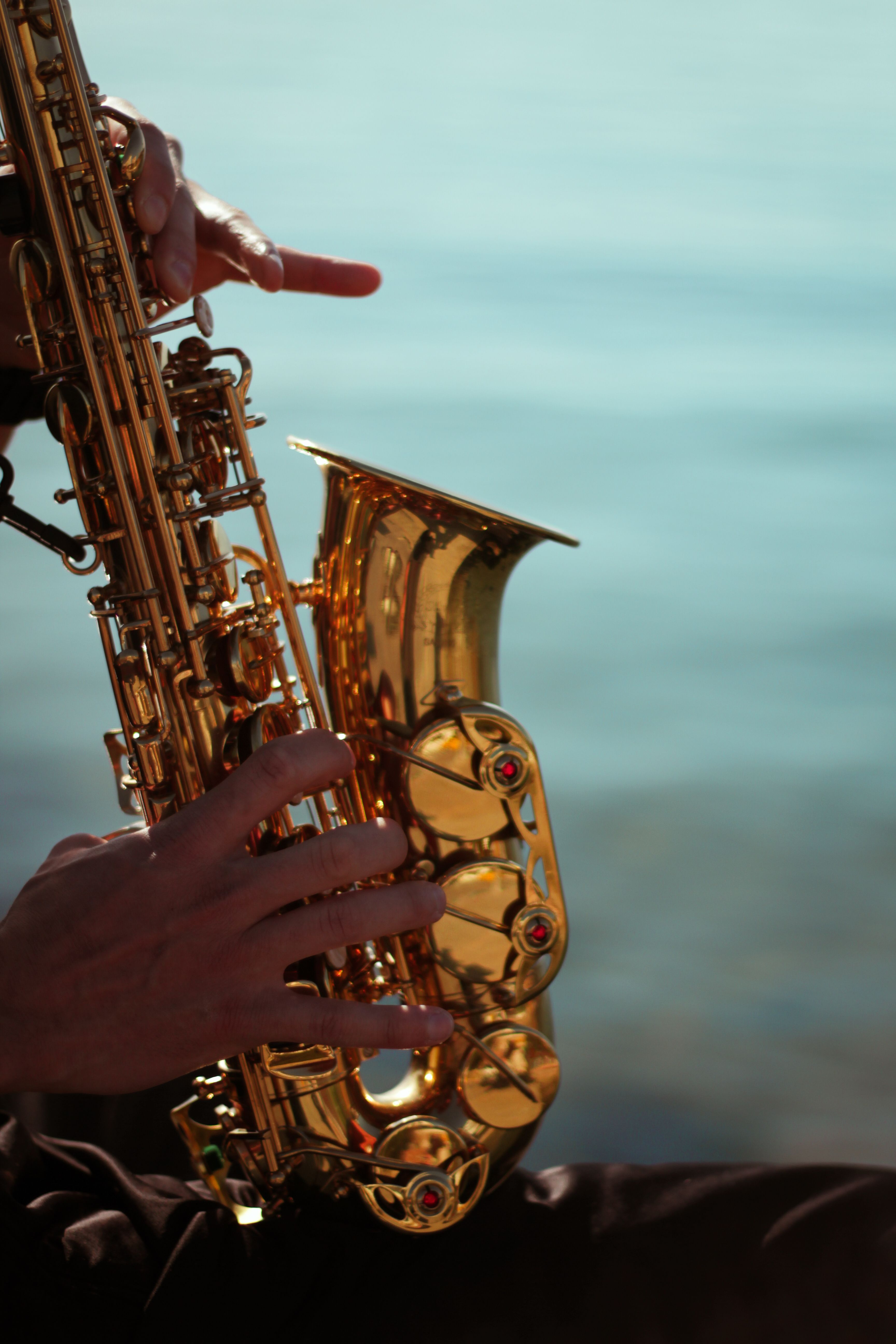 A person playing a saxophone near the water · Free Stock Photo