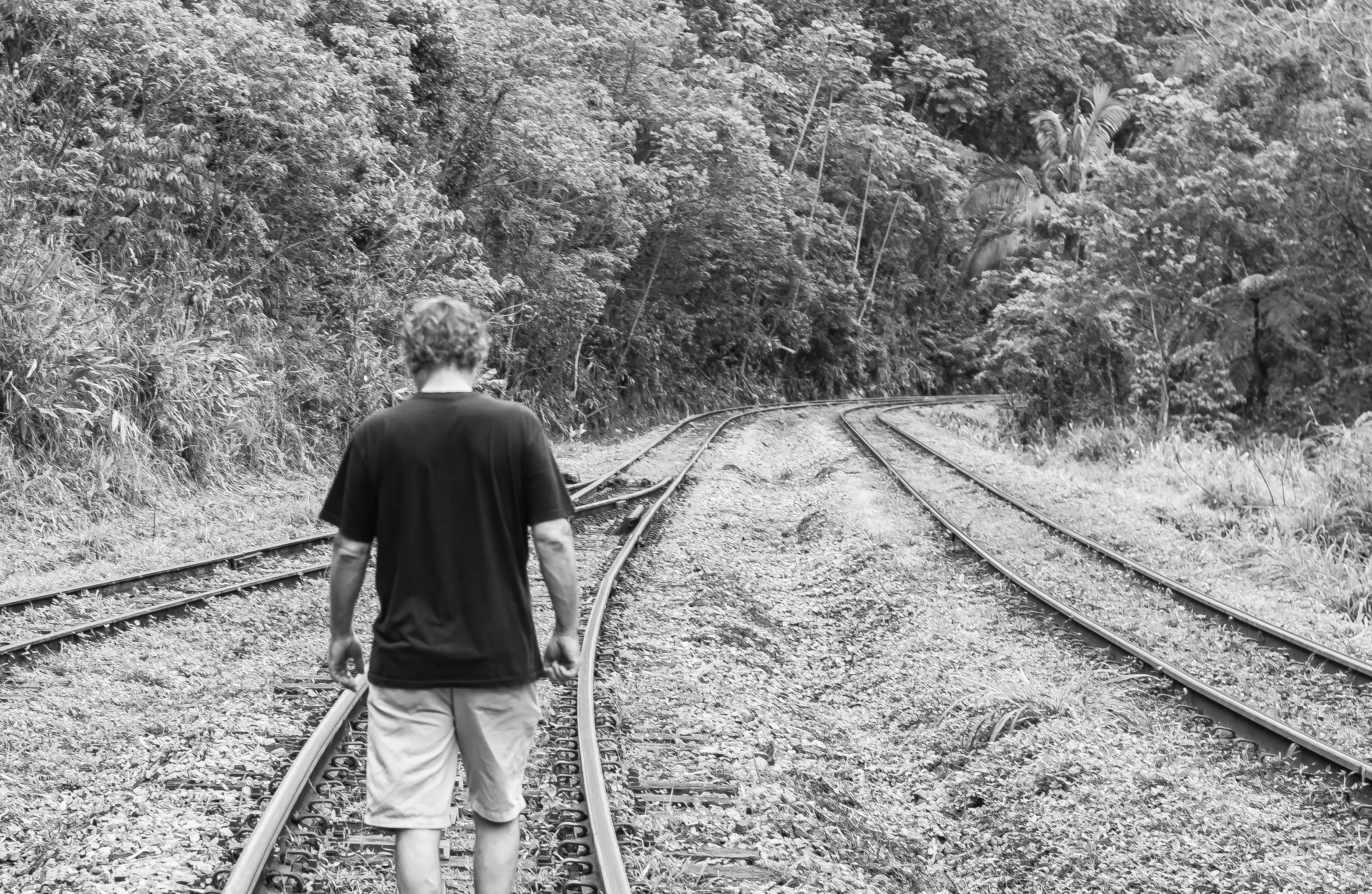 A man walking down the tracks in black and white · Free Stock Photo