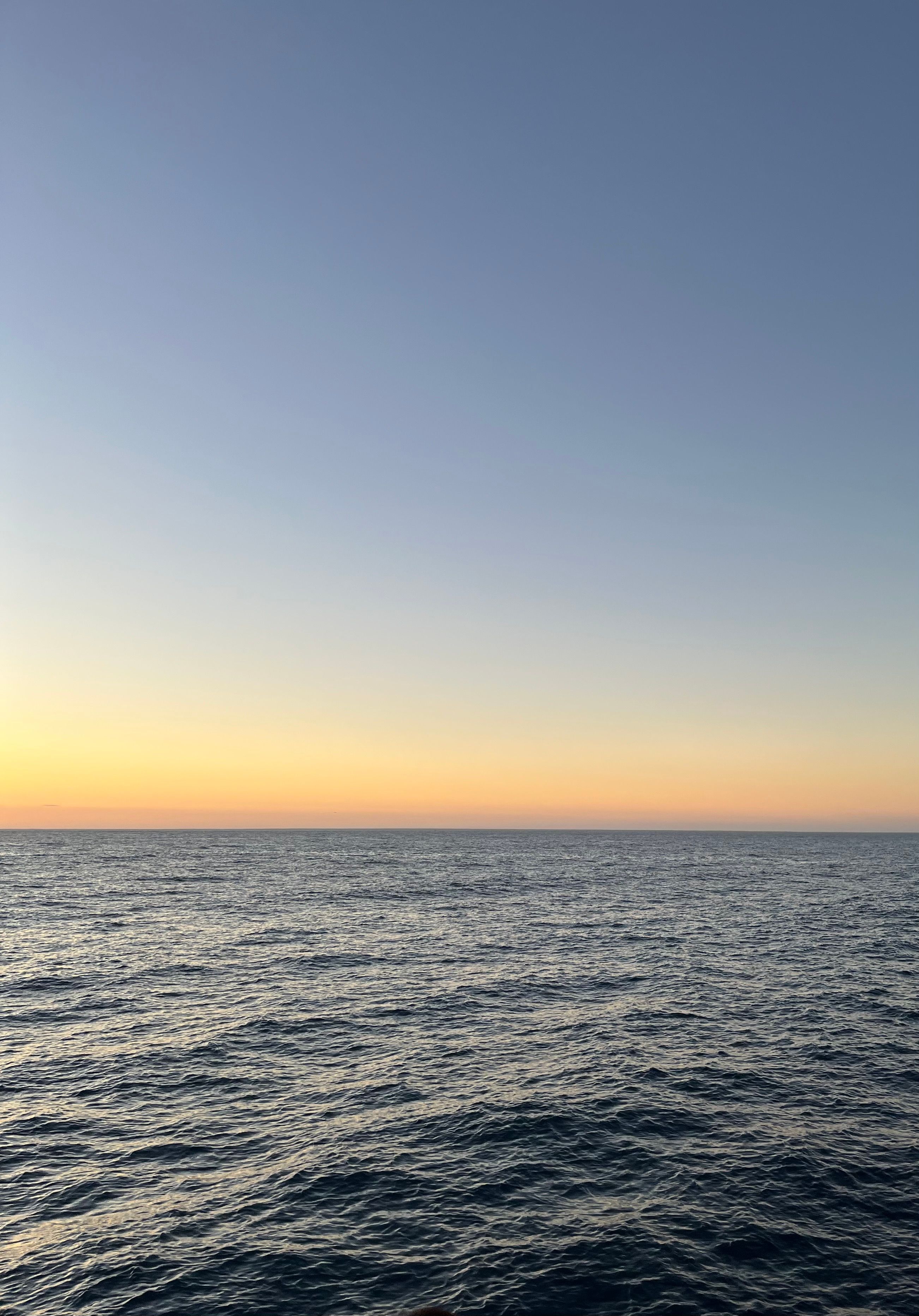 A sunset over the ocean with a boat in the distance · Free Stock Photo