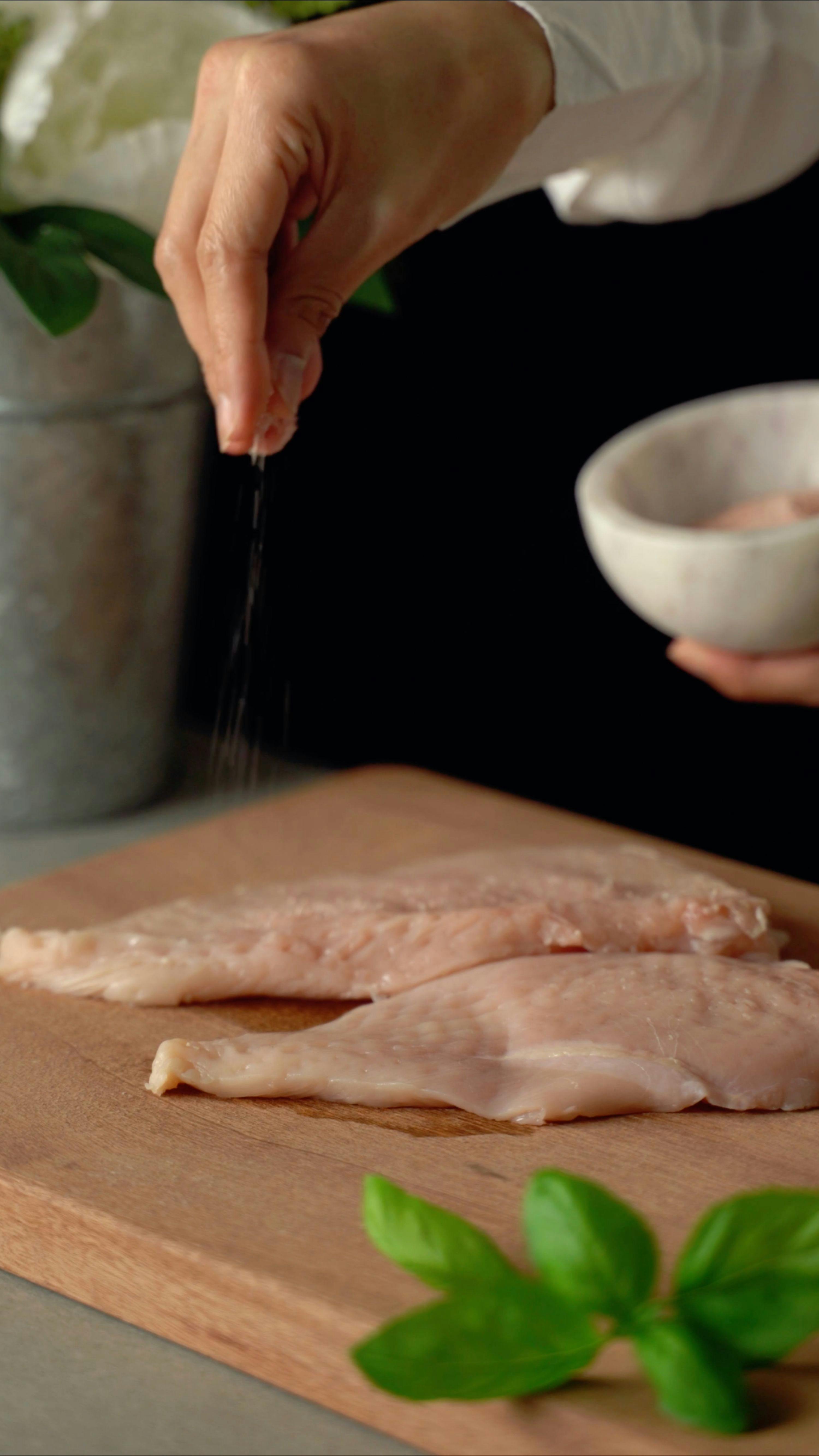 A person sprinkling basil on some chicken · Free Stock Photo
