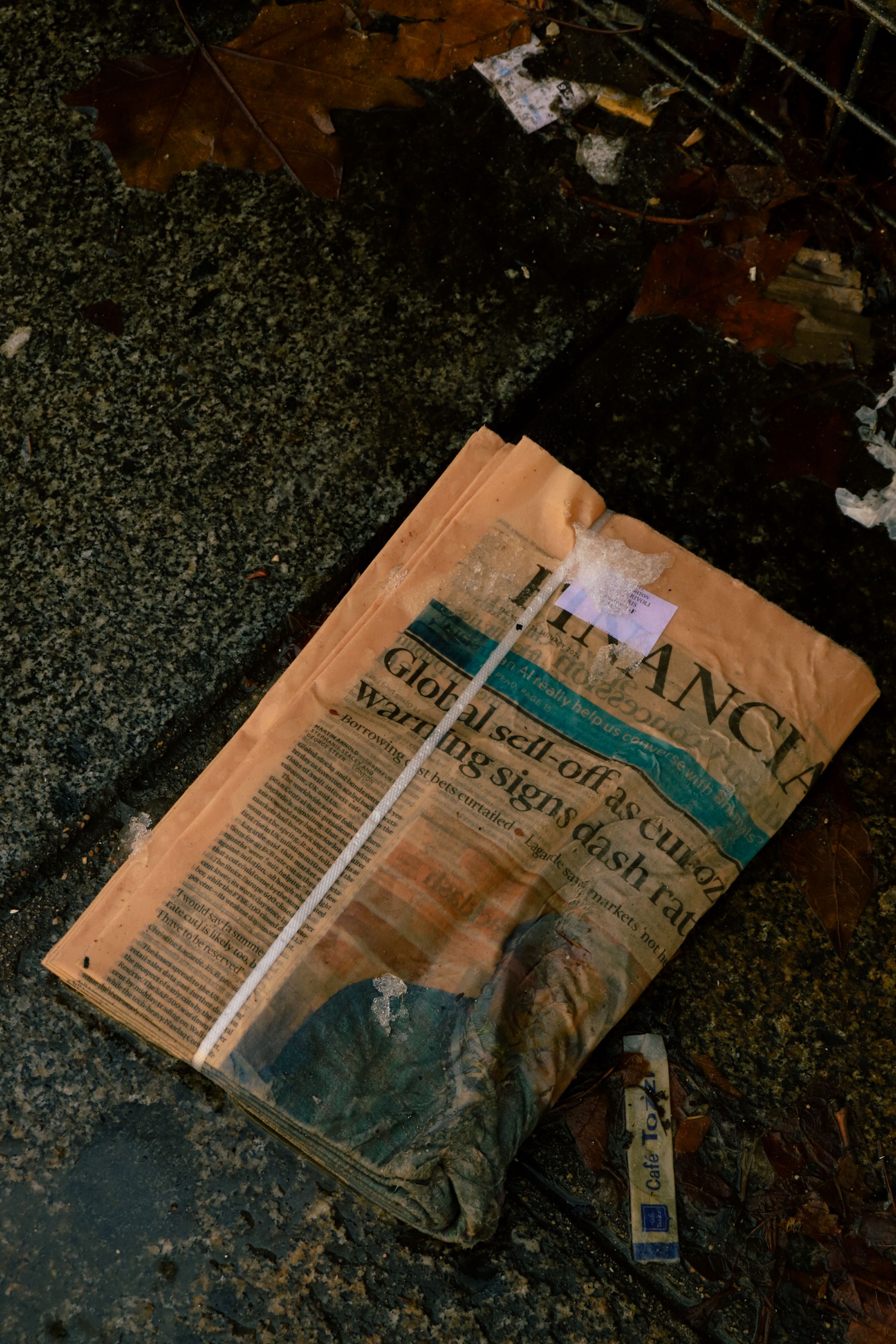 A newspaper laying on the ground next to a trash can · Free Stock Photo