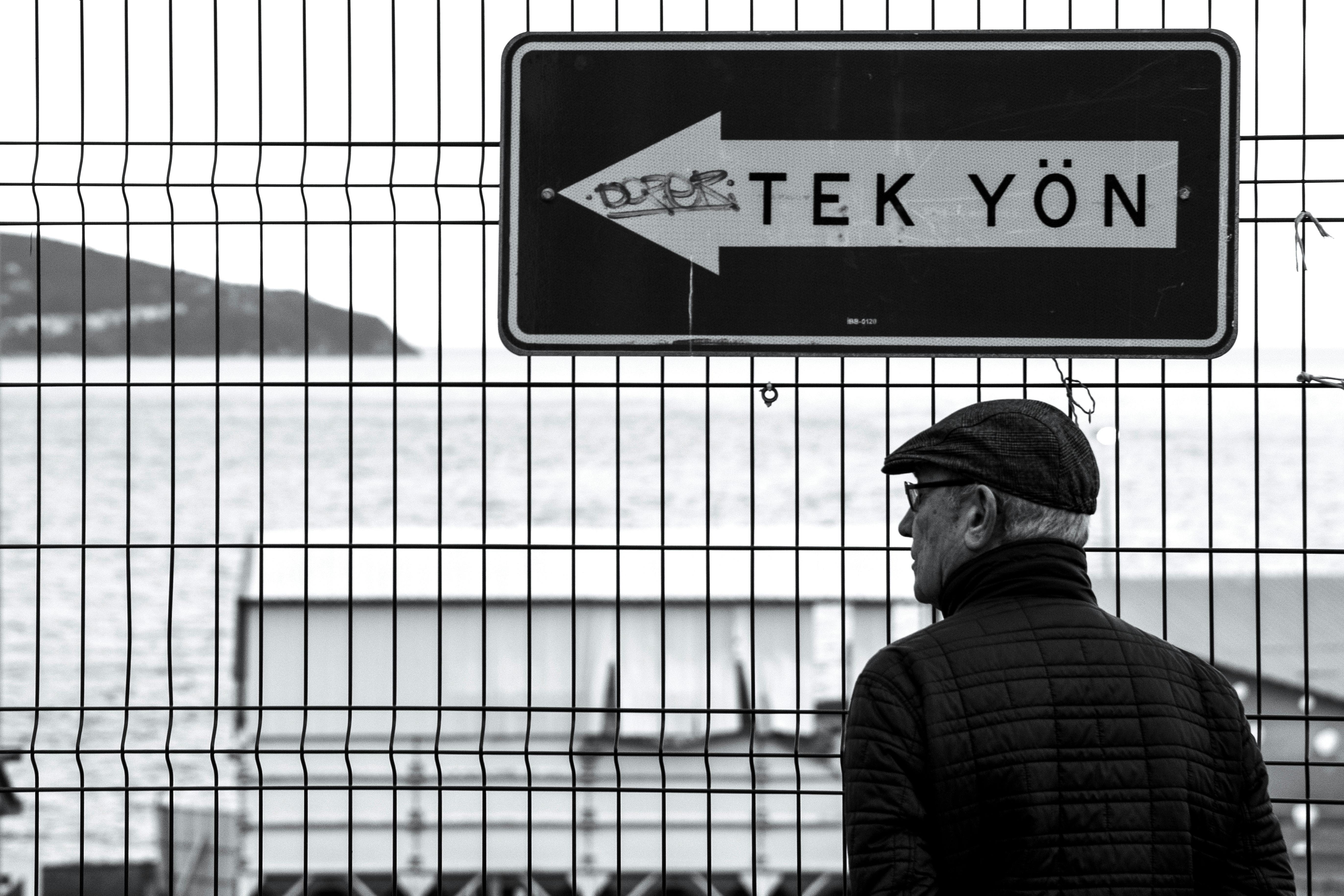 Elderly Man Standing by Directional Sign on Fence · Free Stock Photo