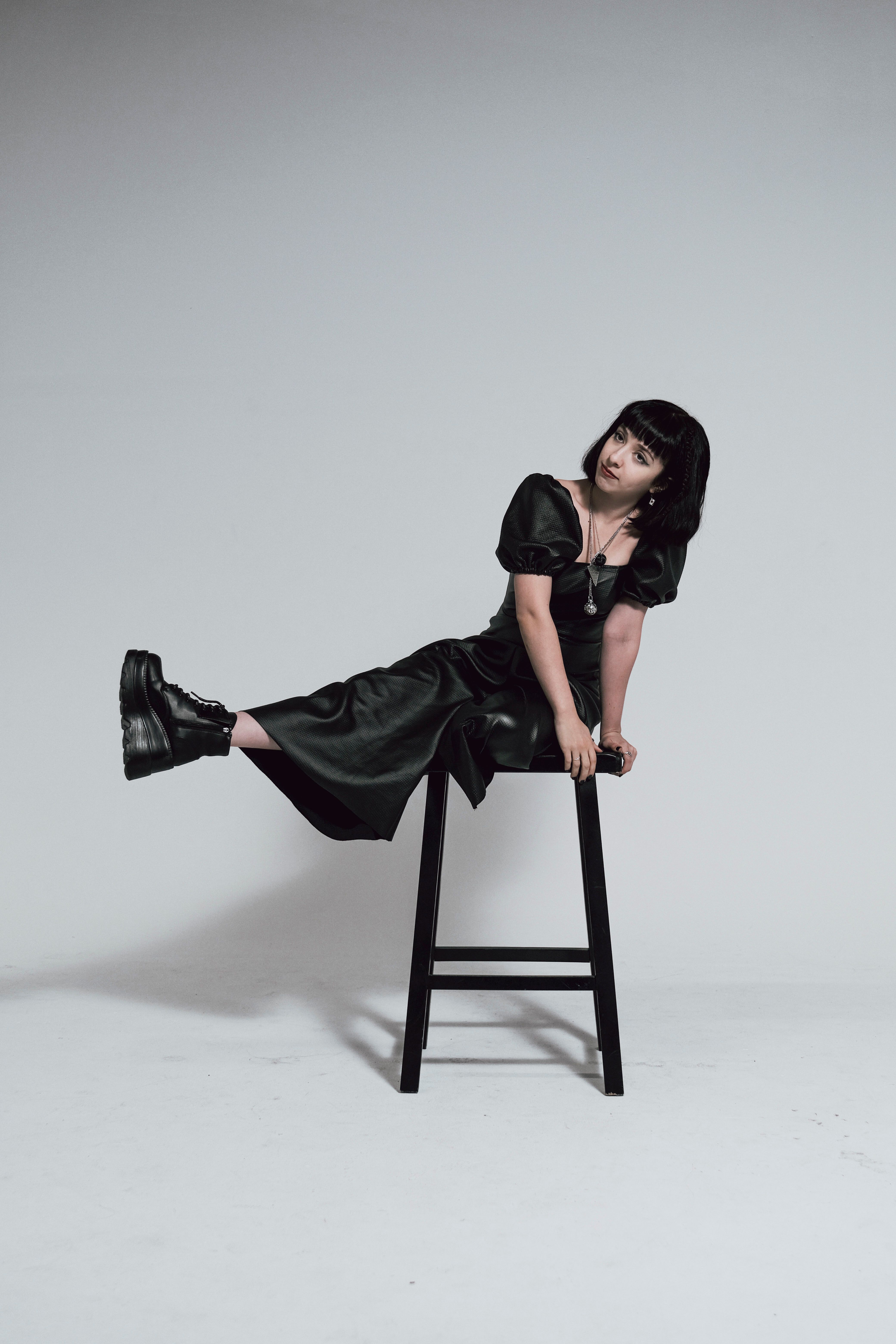 Young Woman in a Black Dress and Boots Sitting on a Stool · Free Stock ...