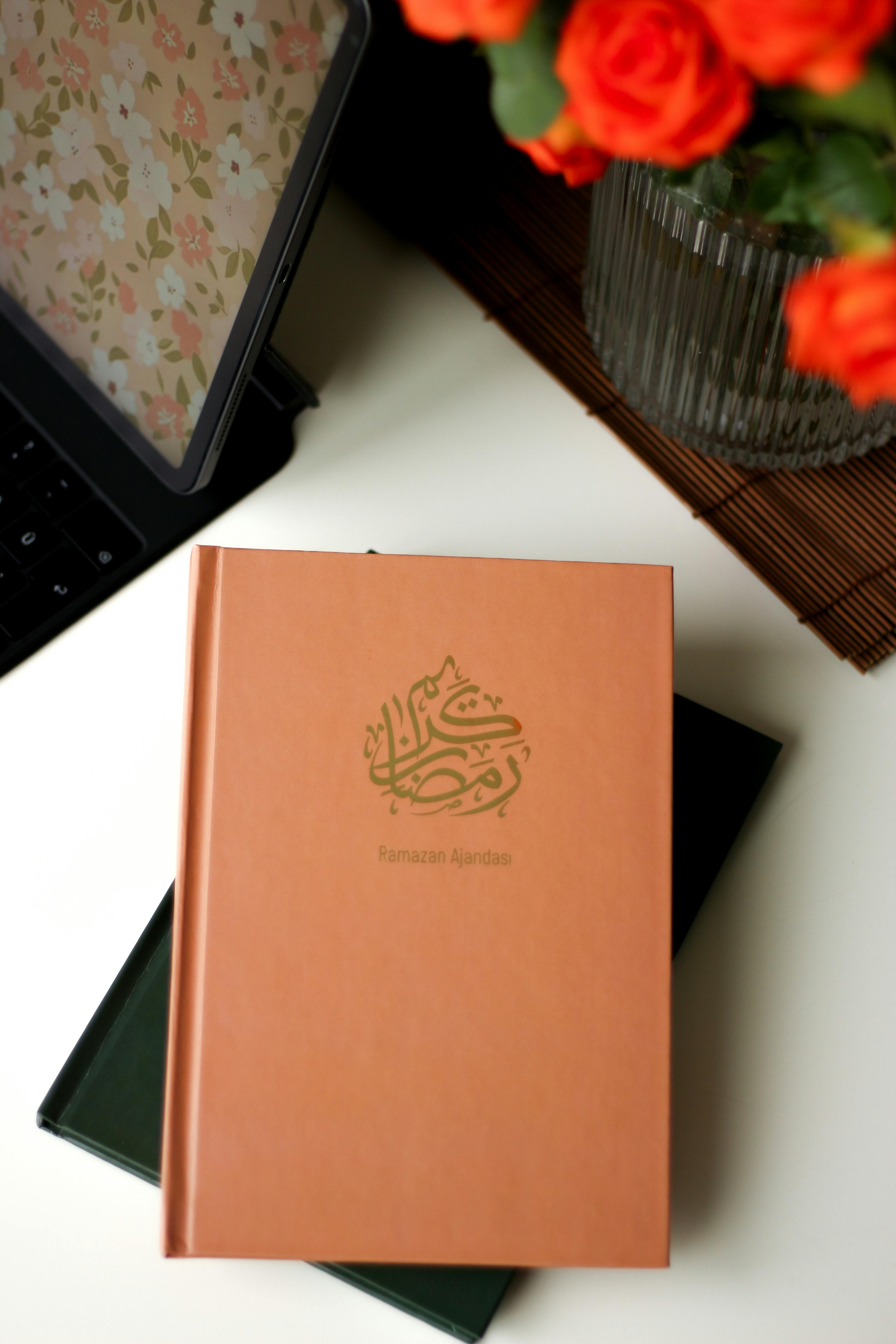 A book with islamic writing on it sitting on a table next to a laptop ...